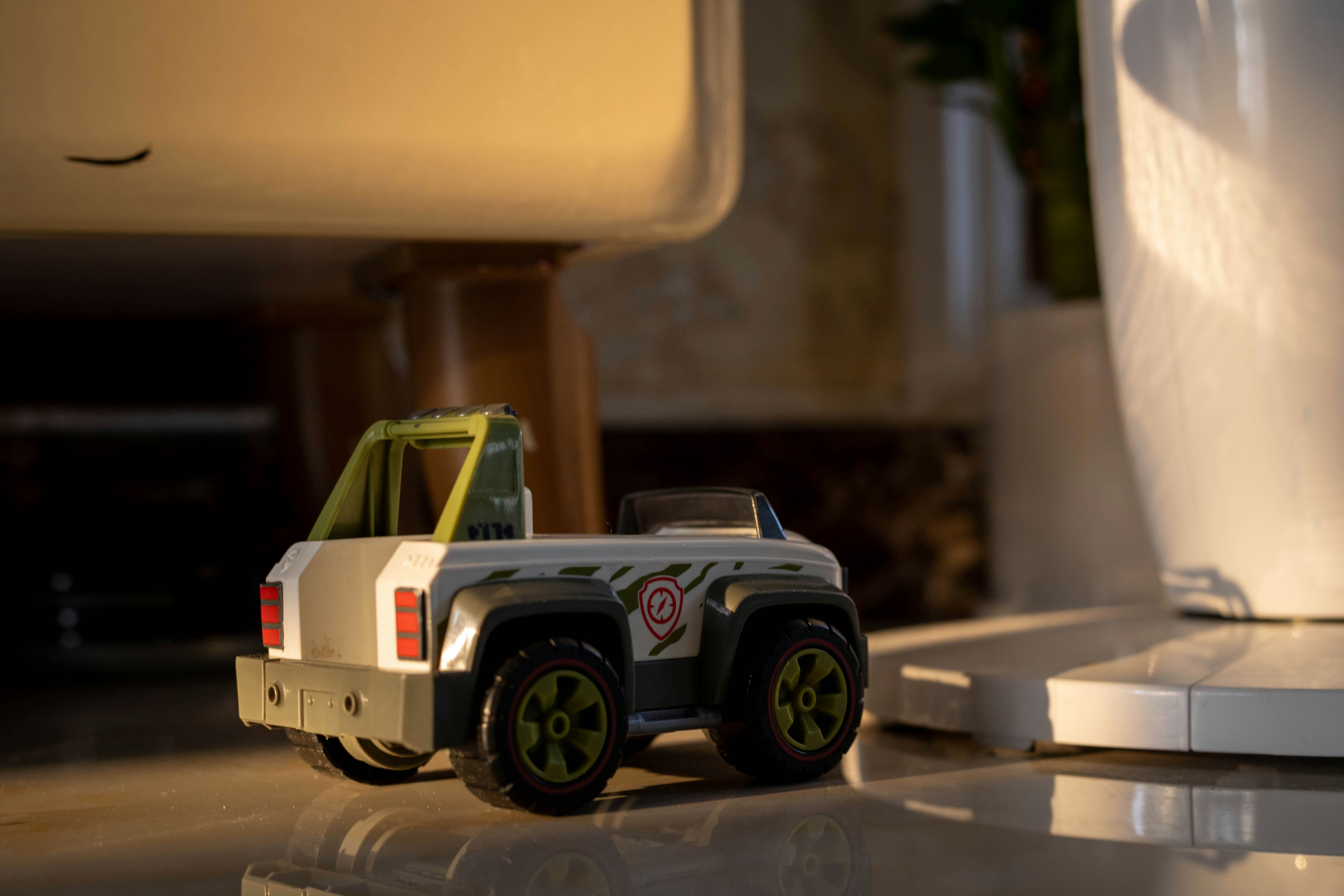 A toy vehicle positioned on a reflective surface, illuminated by warm sunlight, casting intriguing shadows. The scene captures a moment of childhood imagination.