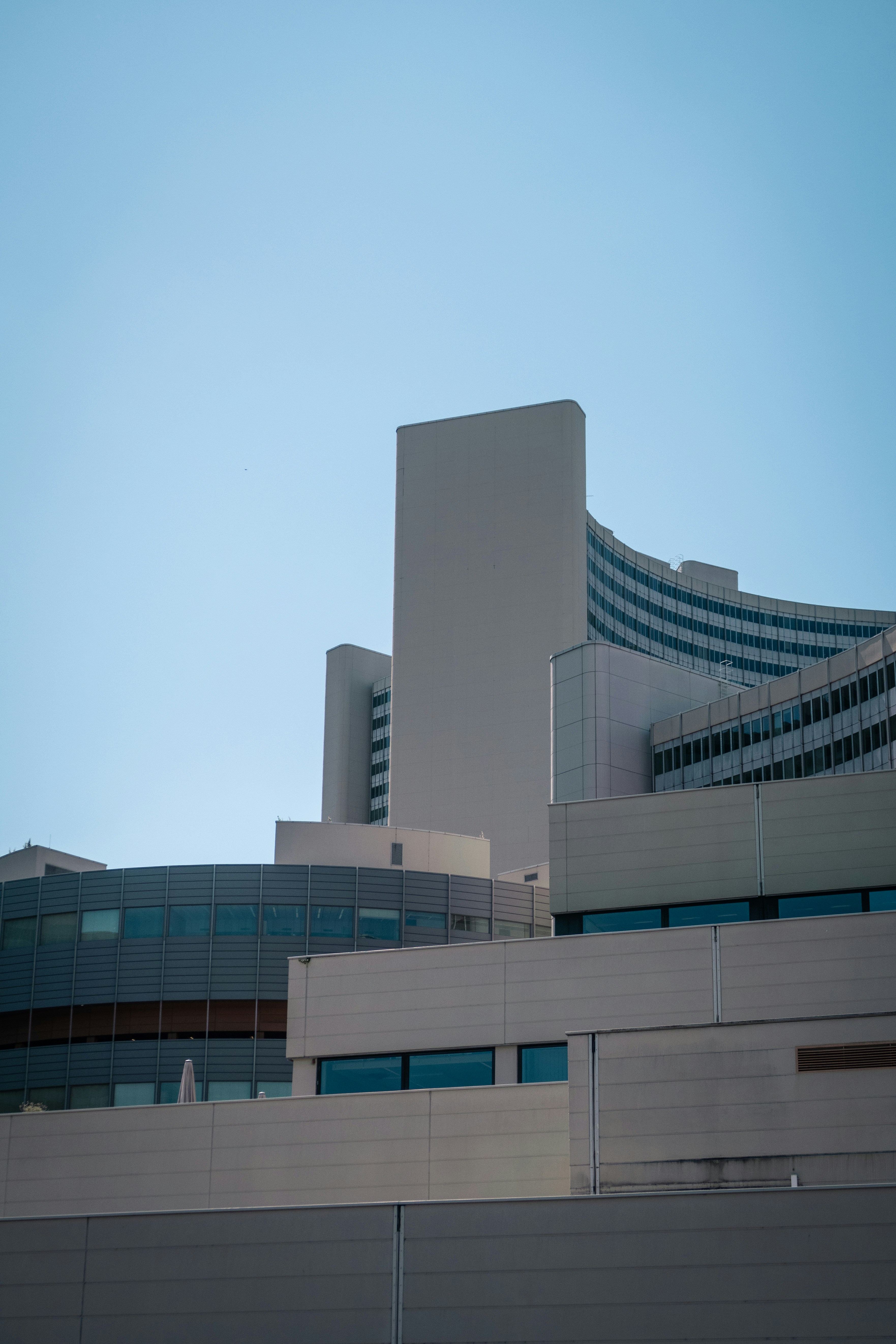 A contemporary building with angular shapes and large glass windows, set against a clear blue sky. The design showcases a blend of textures and lines.