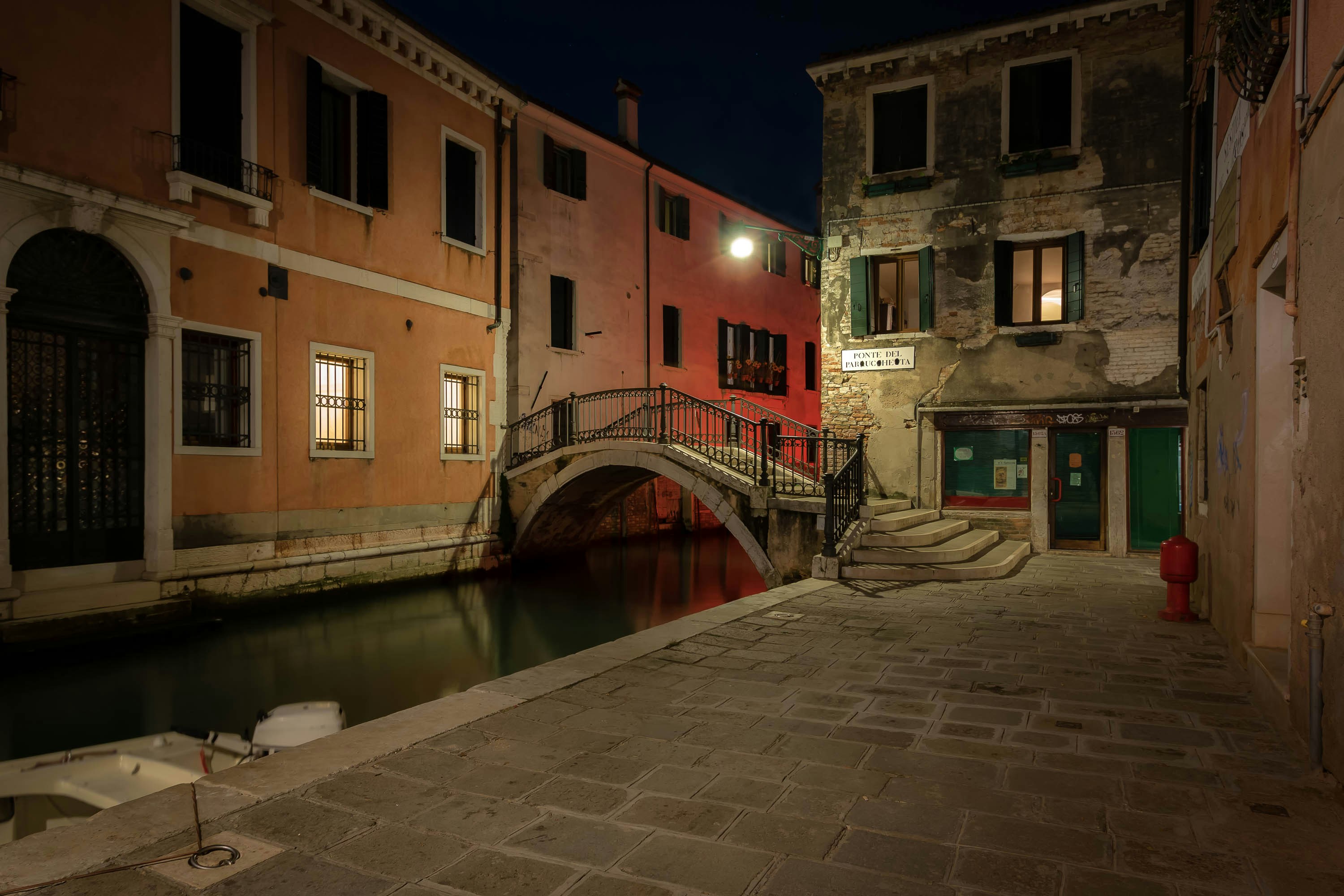 Quiet canal scene in Venice featuring a charming bridge and colorful buildings illuminated by soft streetlights.
