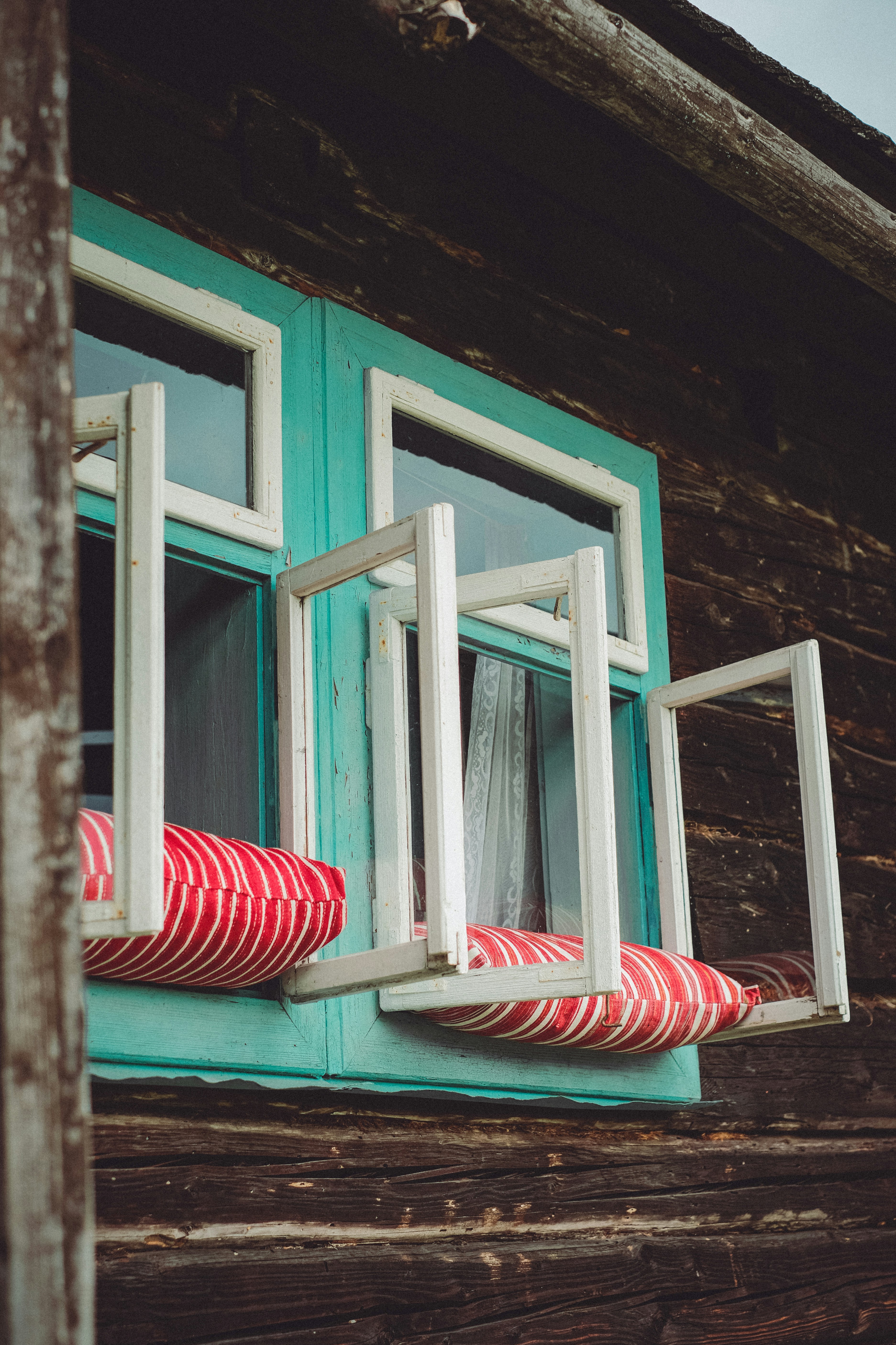 Teal Window Frames and Red Cushions on a Weathered Cabin