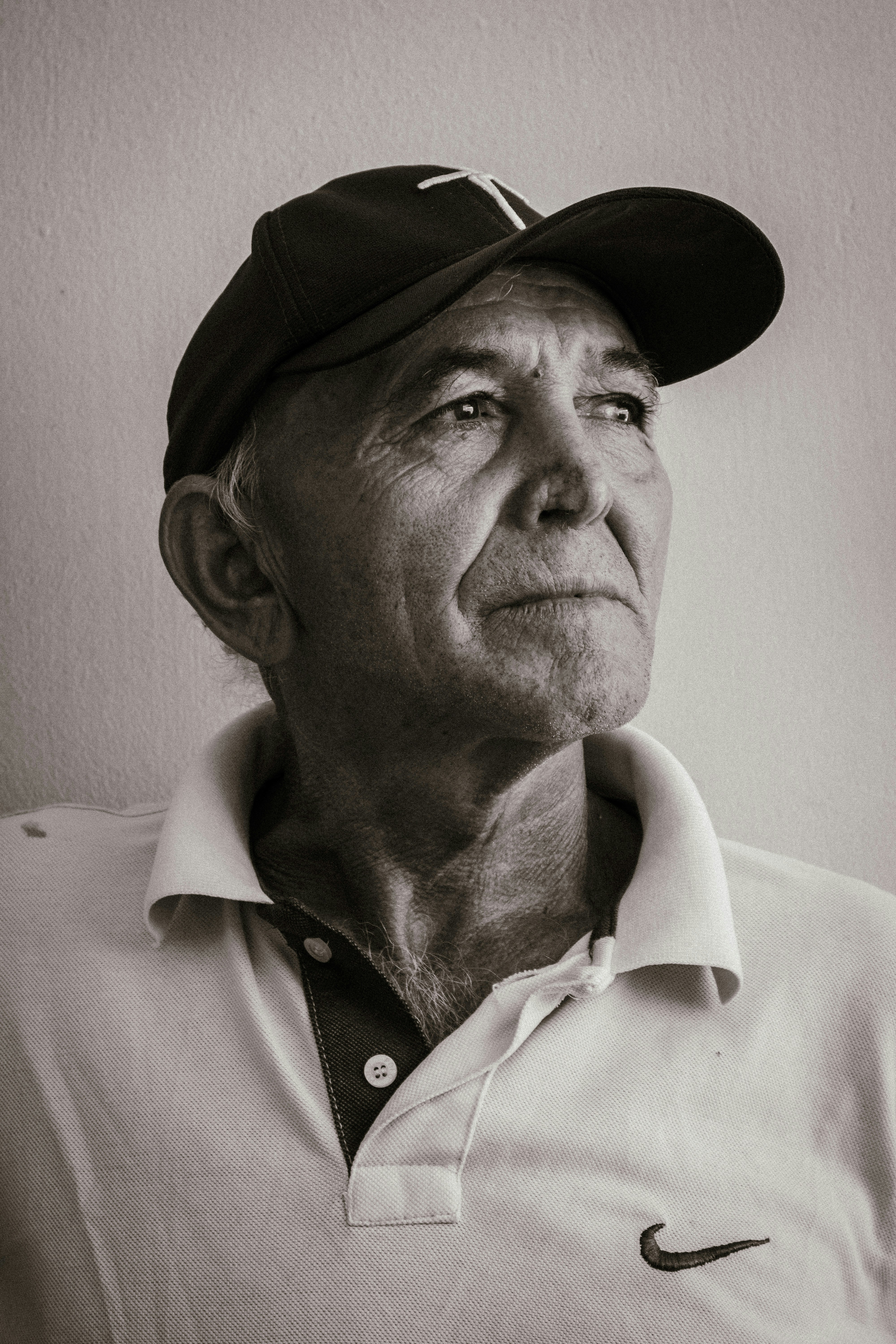 Elderly man in a cap gazes thoughtfully, showcasing deep lines of experience and wisdom against a neutral background.