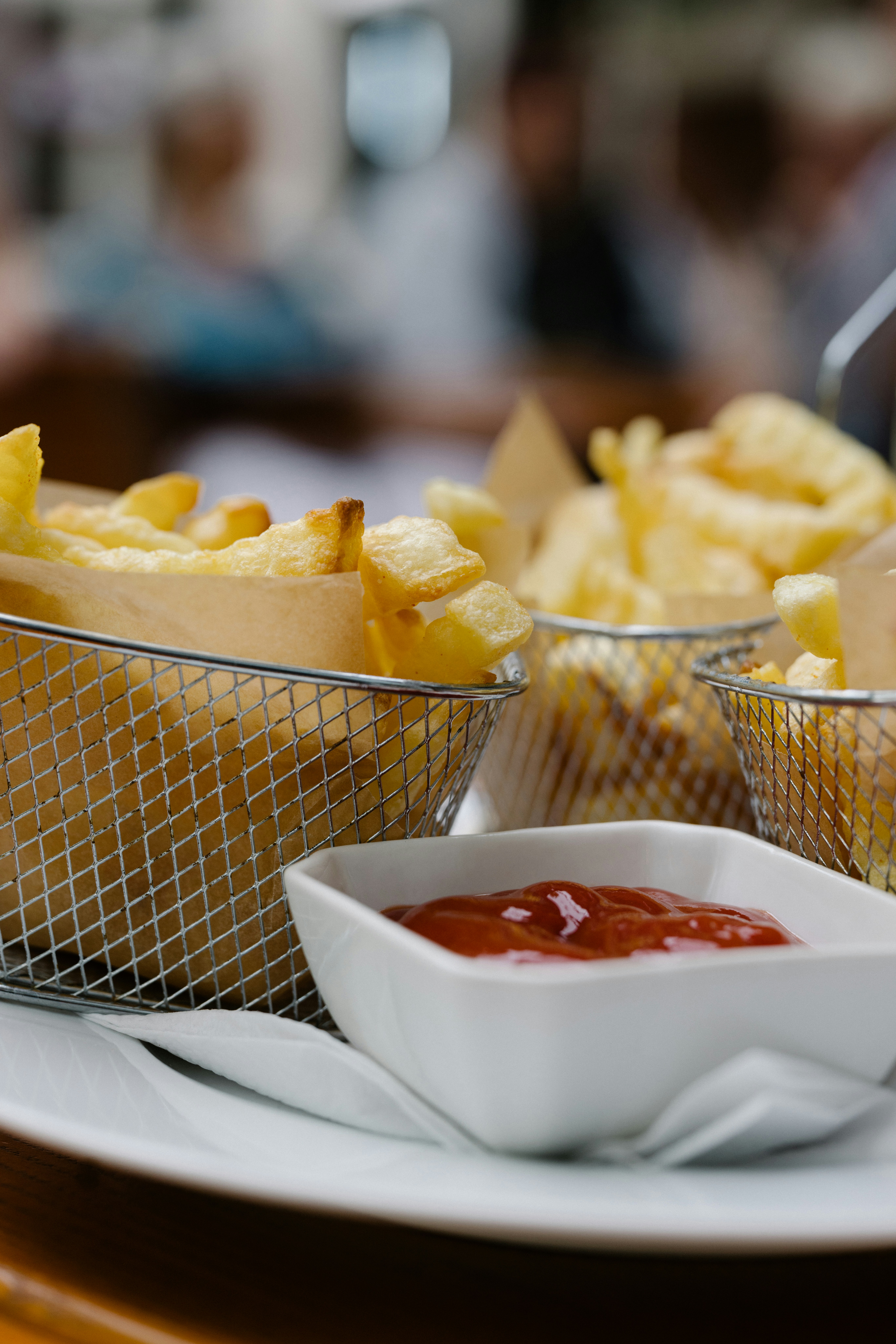 Golden fries served in wire baskets alongside a small bowl of ketchup on a white plate.