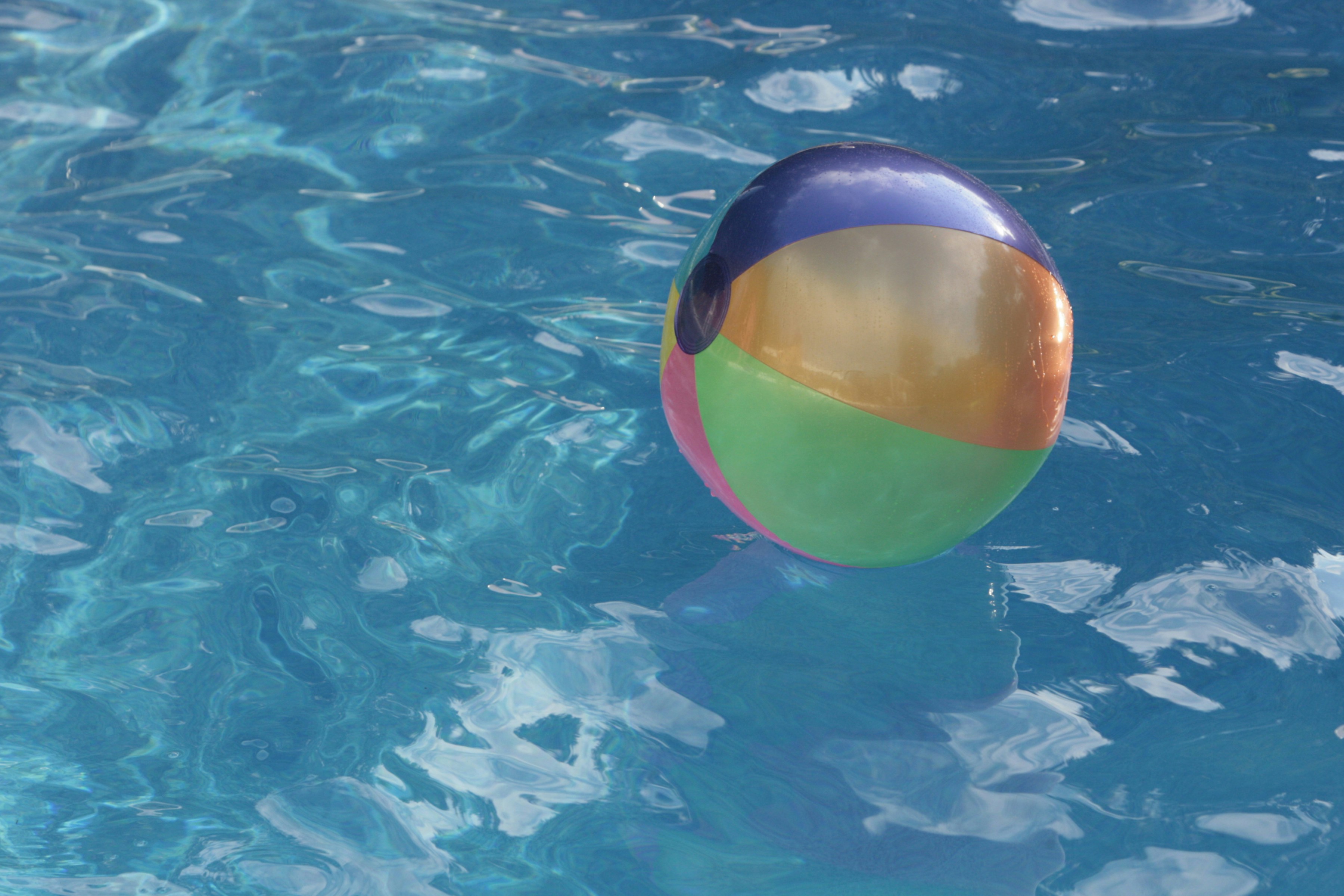 A colorful beach ball floats serenely on the surface of a shimmering blue pool, reflecting the sunlight. This playful scene captures the essence of summer leisure.