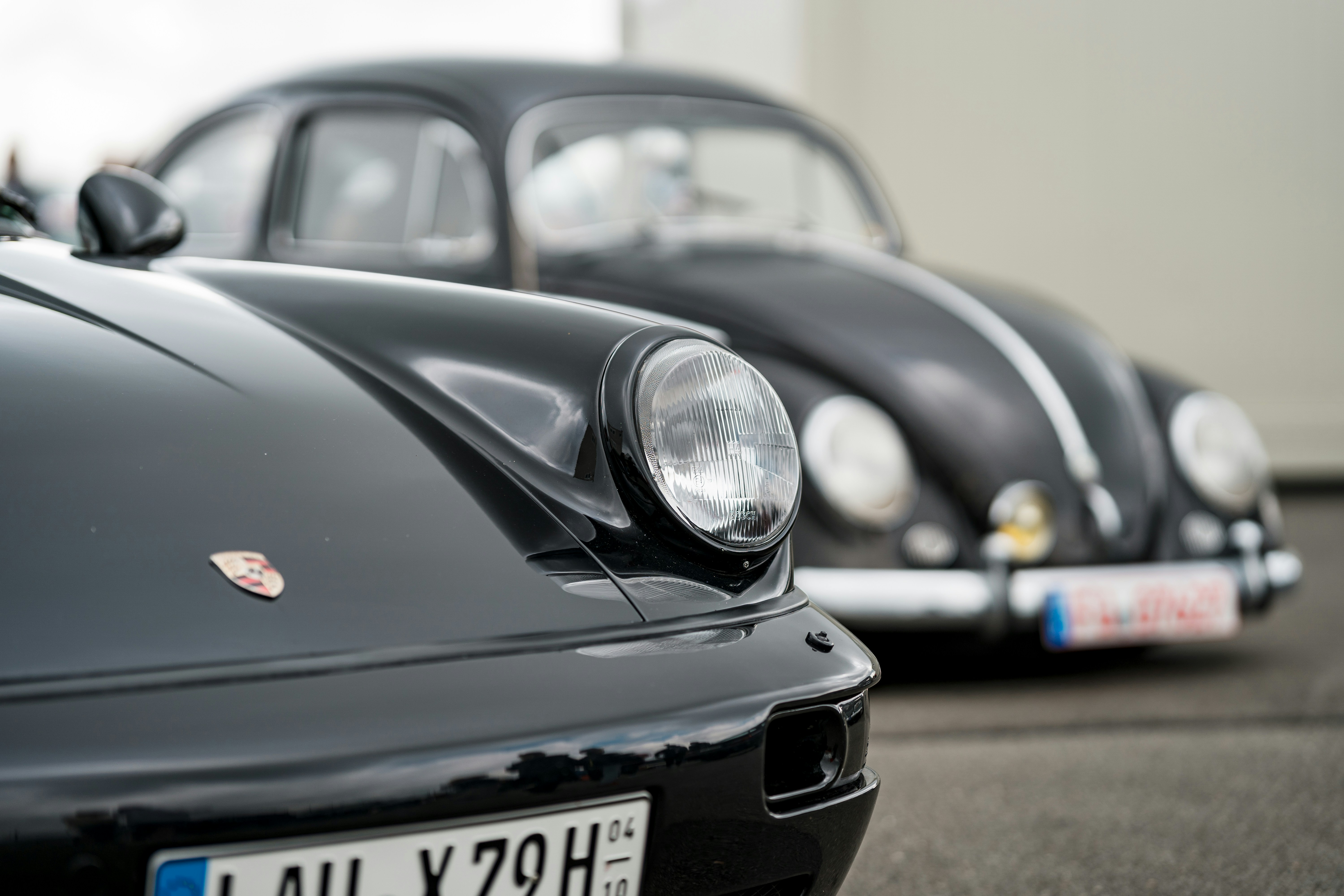 Close-up of a classic Porsche front with a vintage Volkswagen Beetle blurred in the background.