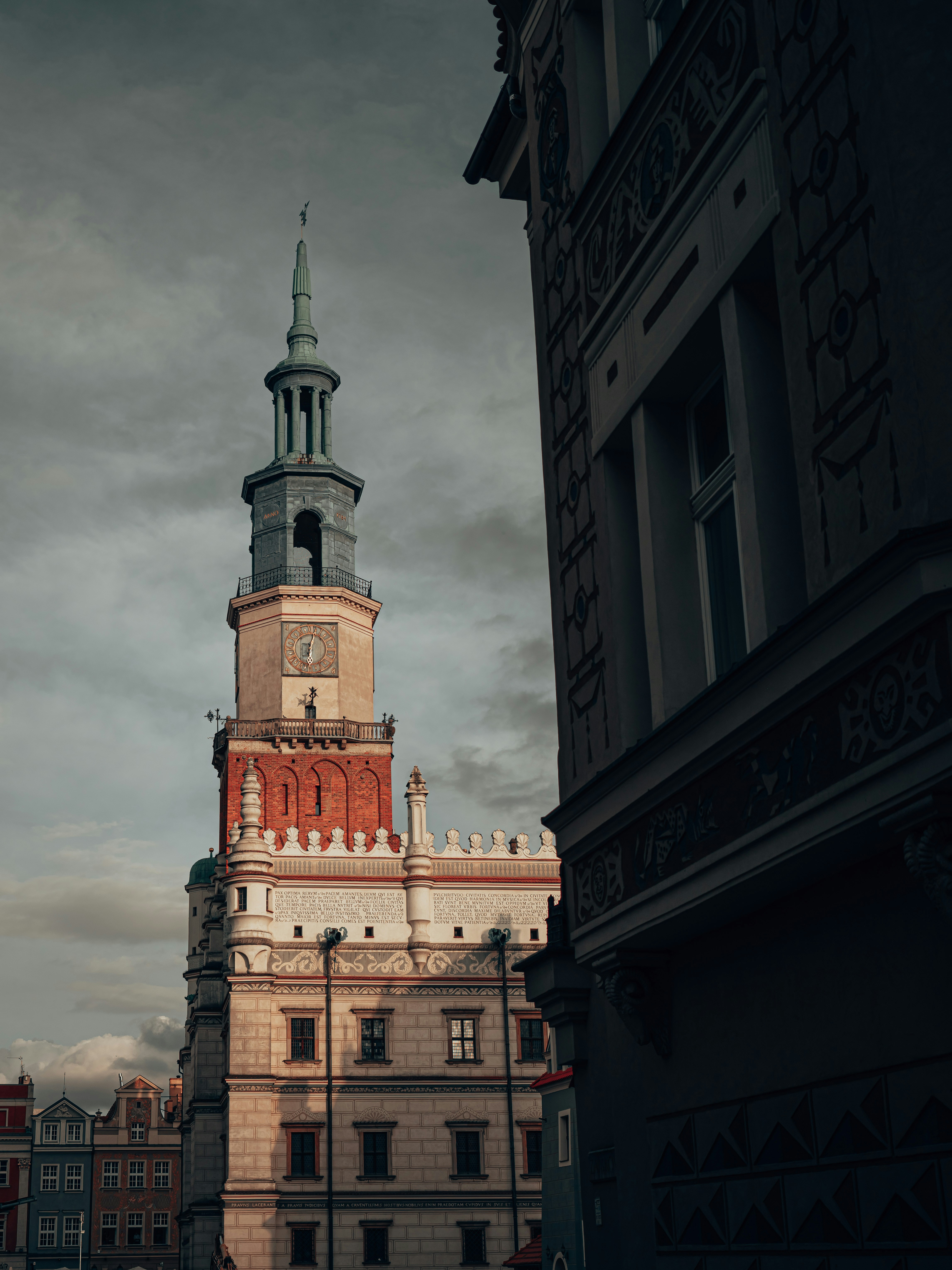 Historic tower adorned with intricate architectural details, framed by neighboring buildings under a moody sky.