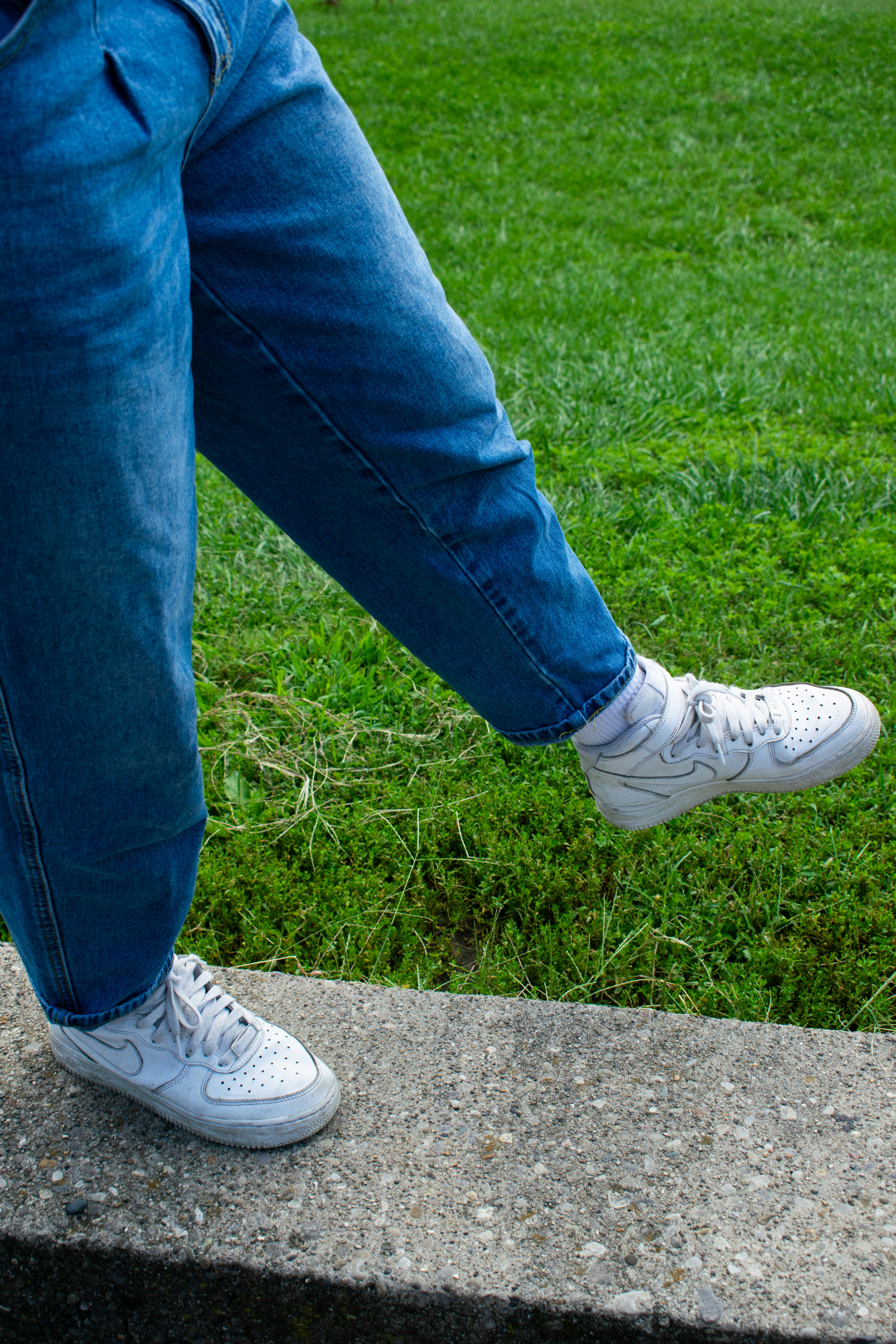 Foot stepping off a concrete edge onto lush green grass, showcasing a casual outdoor moment.