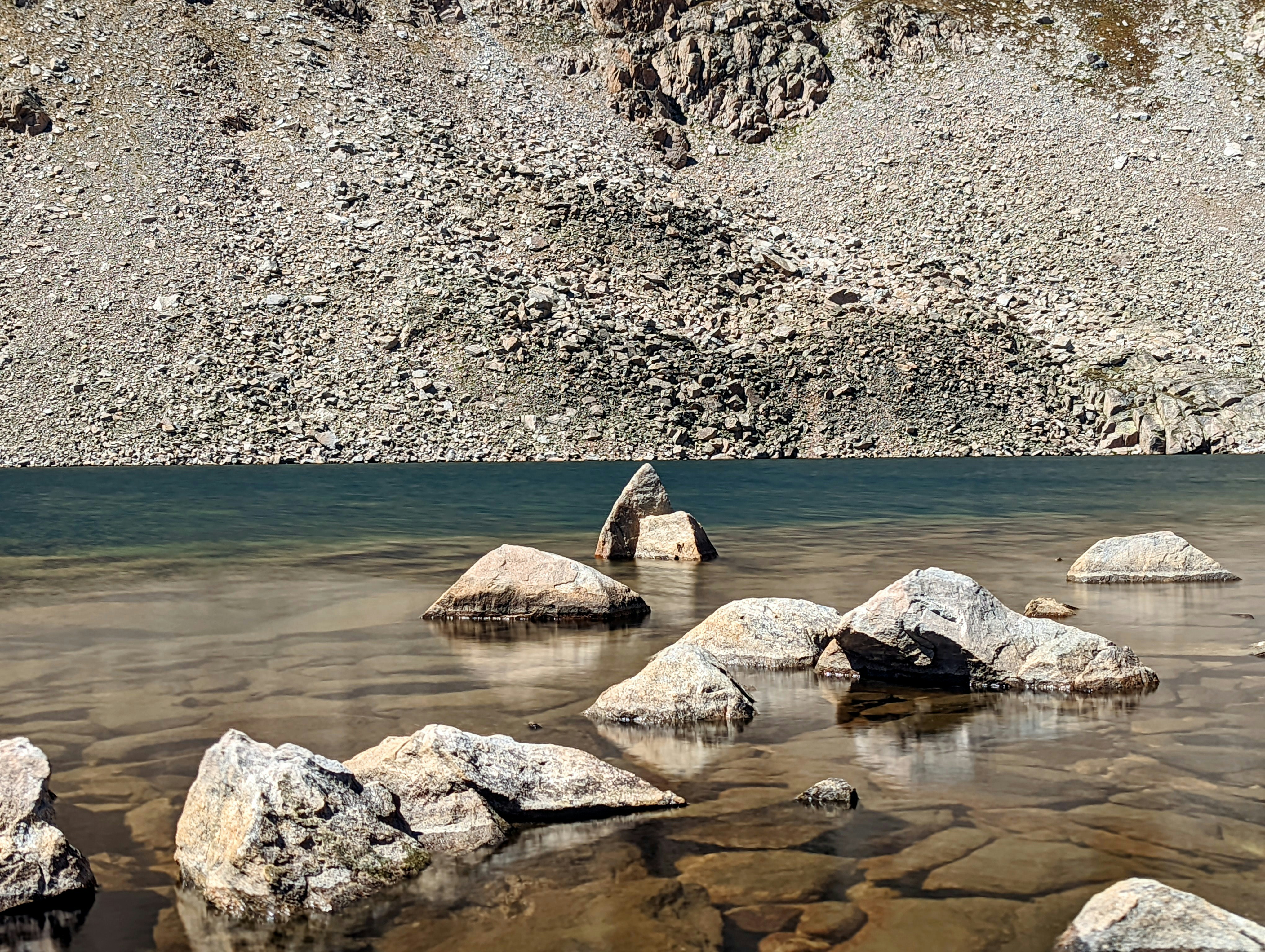 Some rocks sticking out of Bear Lake in Colorado with a towering peak in the background.