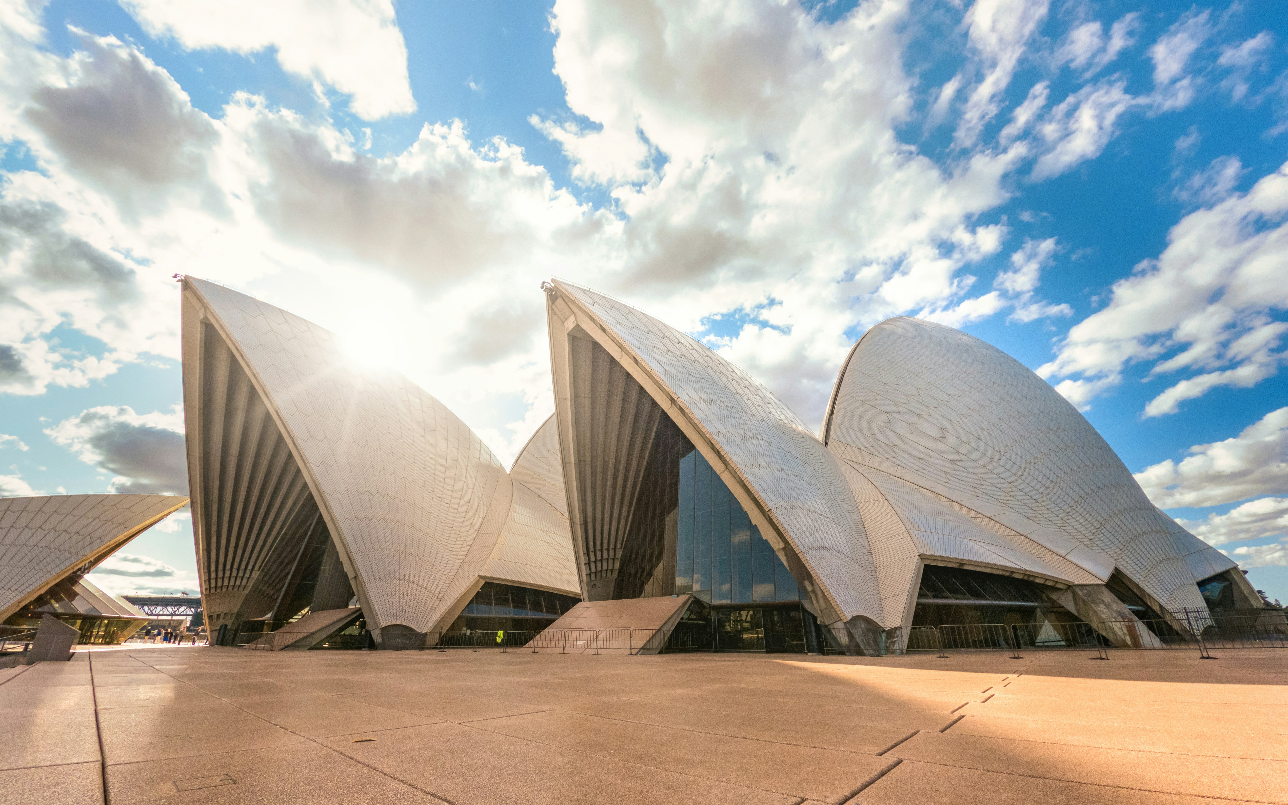 Iconic Sydney Opera House showcasing its distinctive sail-like design against a vibrant sky. The sunlight creates a dramatic effect on the structure.