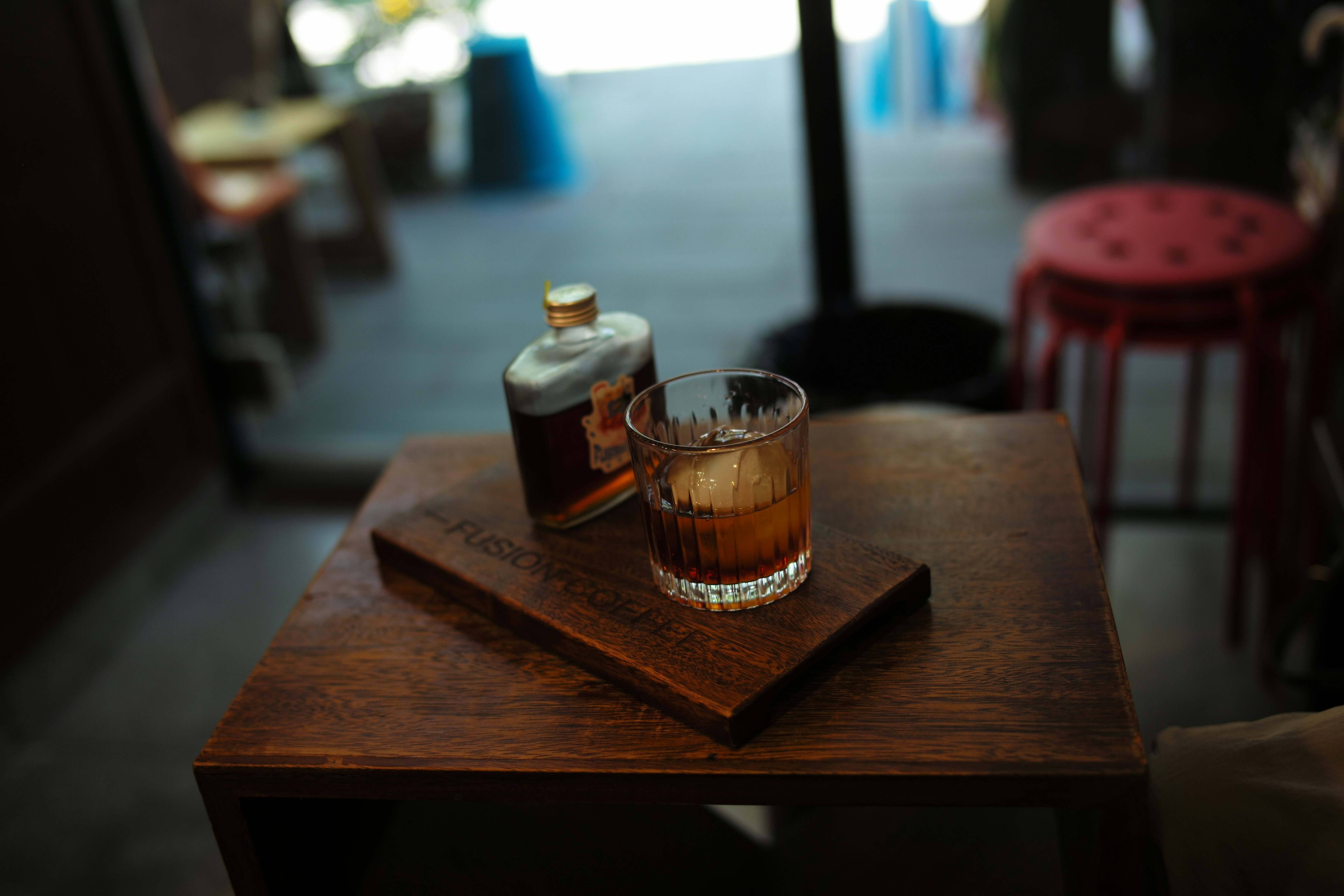 Whiskey glass with ice sits on a wooden table beside a bottle, capturing a cozy atmosphere in a relaxed setting.