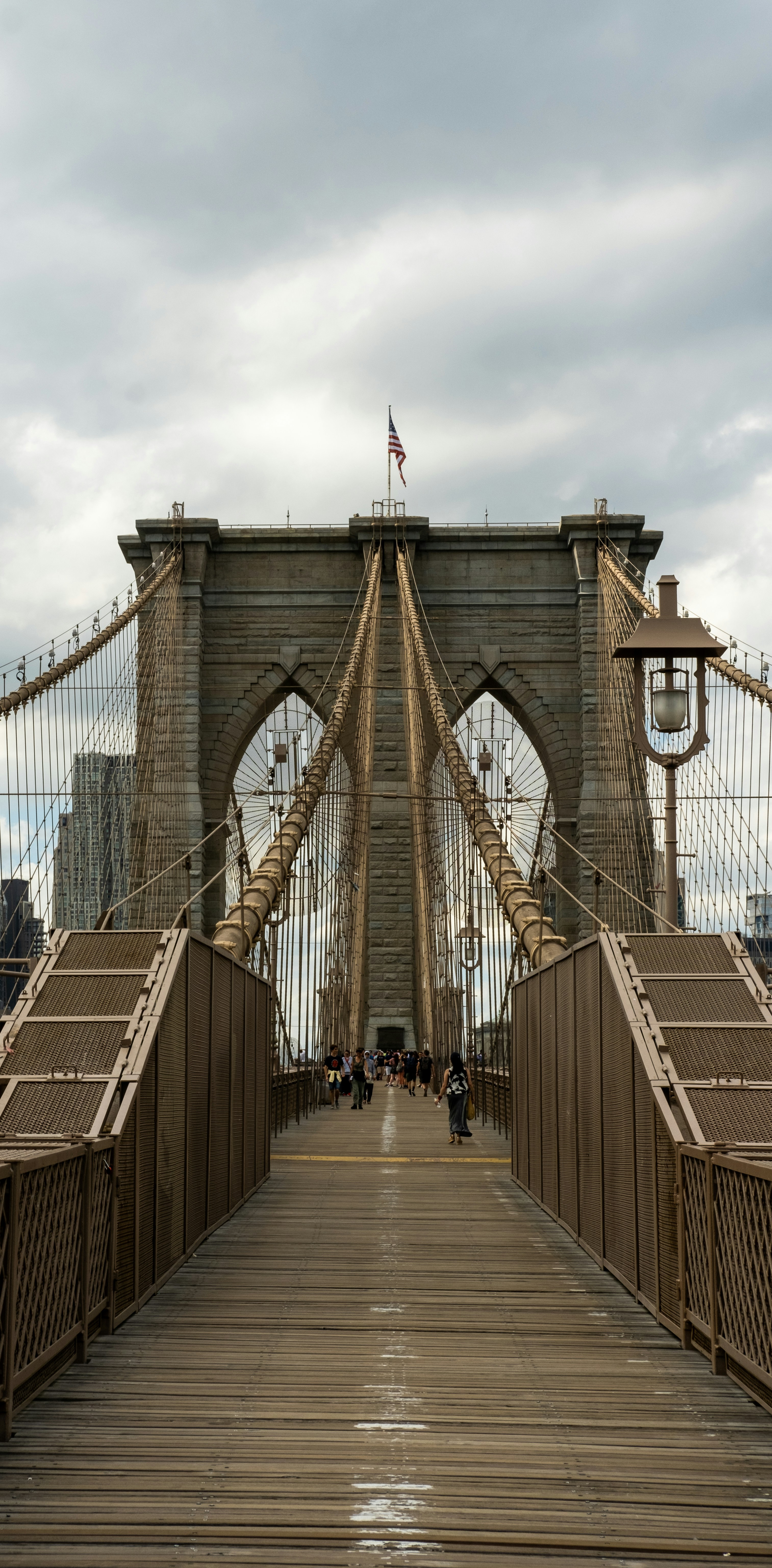 Iconic Brooklyn Bridge stretching over the East River, showcasing its intricate cable work and towering stone arches. A bustling walkway invites pedestrians to cross.