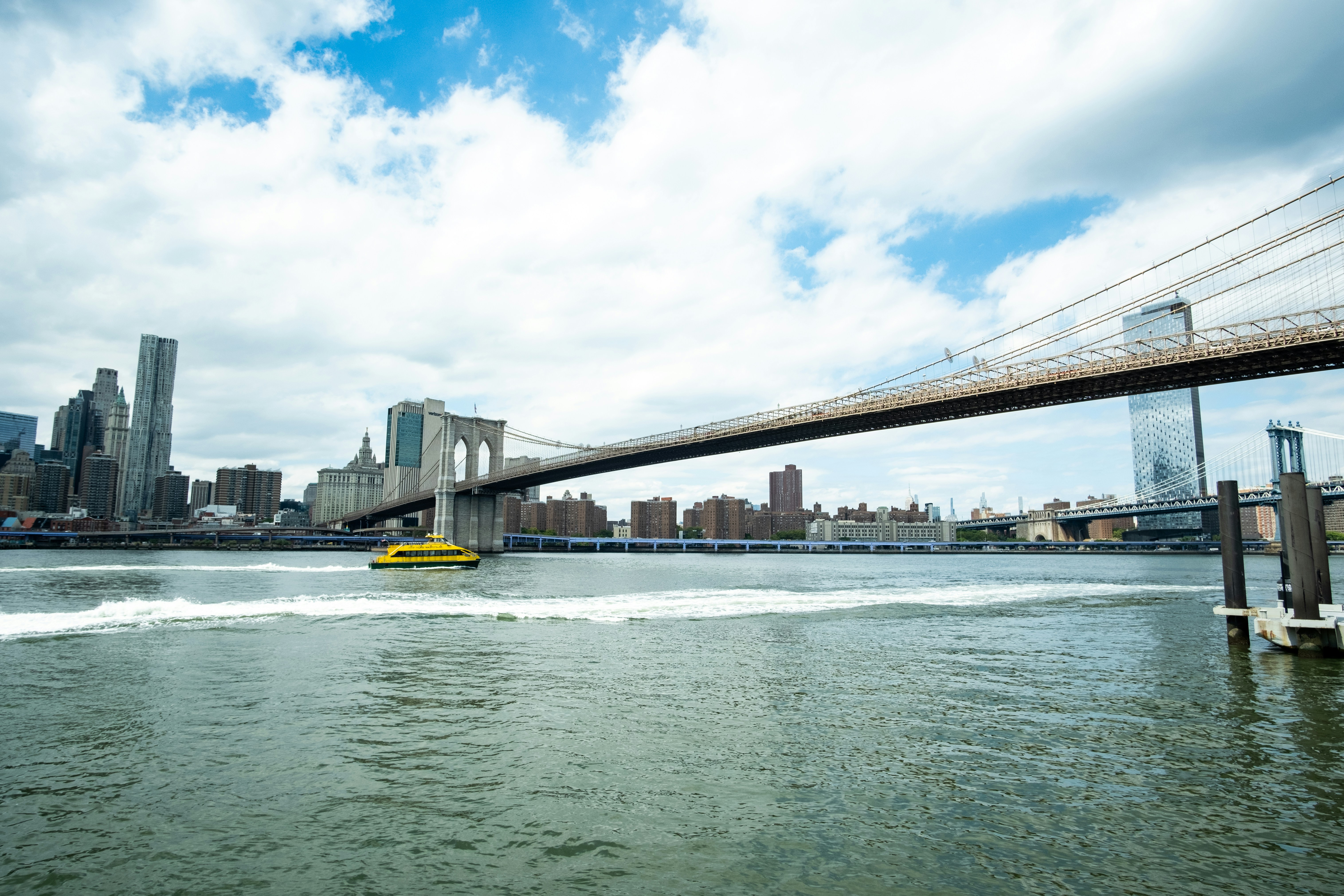 Yellow Water Taxi Crossing the East River Beneath a Cloud-Swept Brooklyn Bridge
