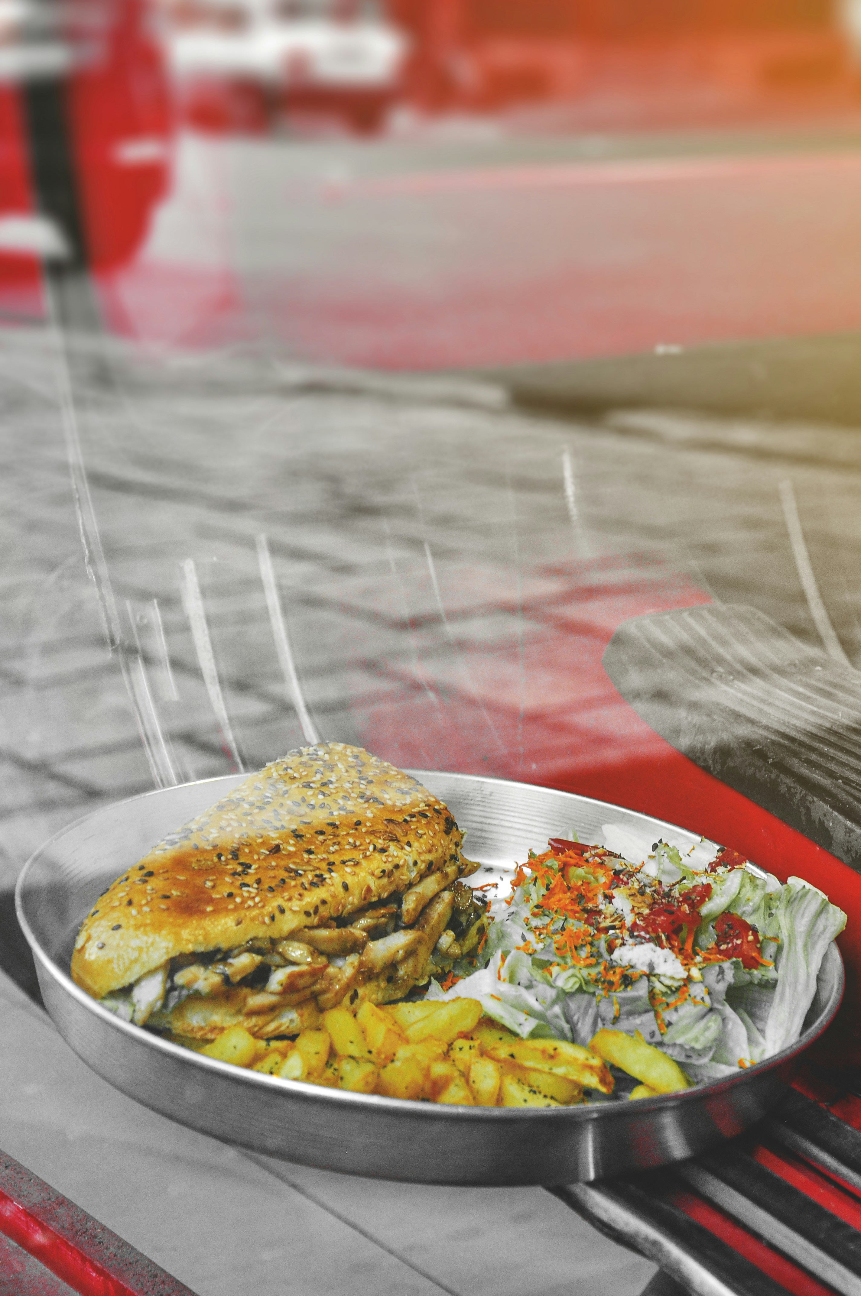 Plate of sandwich and salad on a street-side grill, with rain streaks and a blurred red backdrop