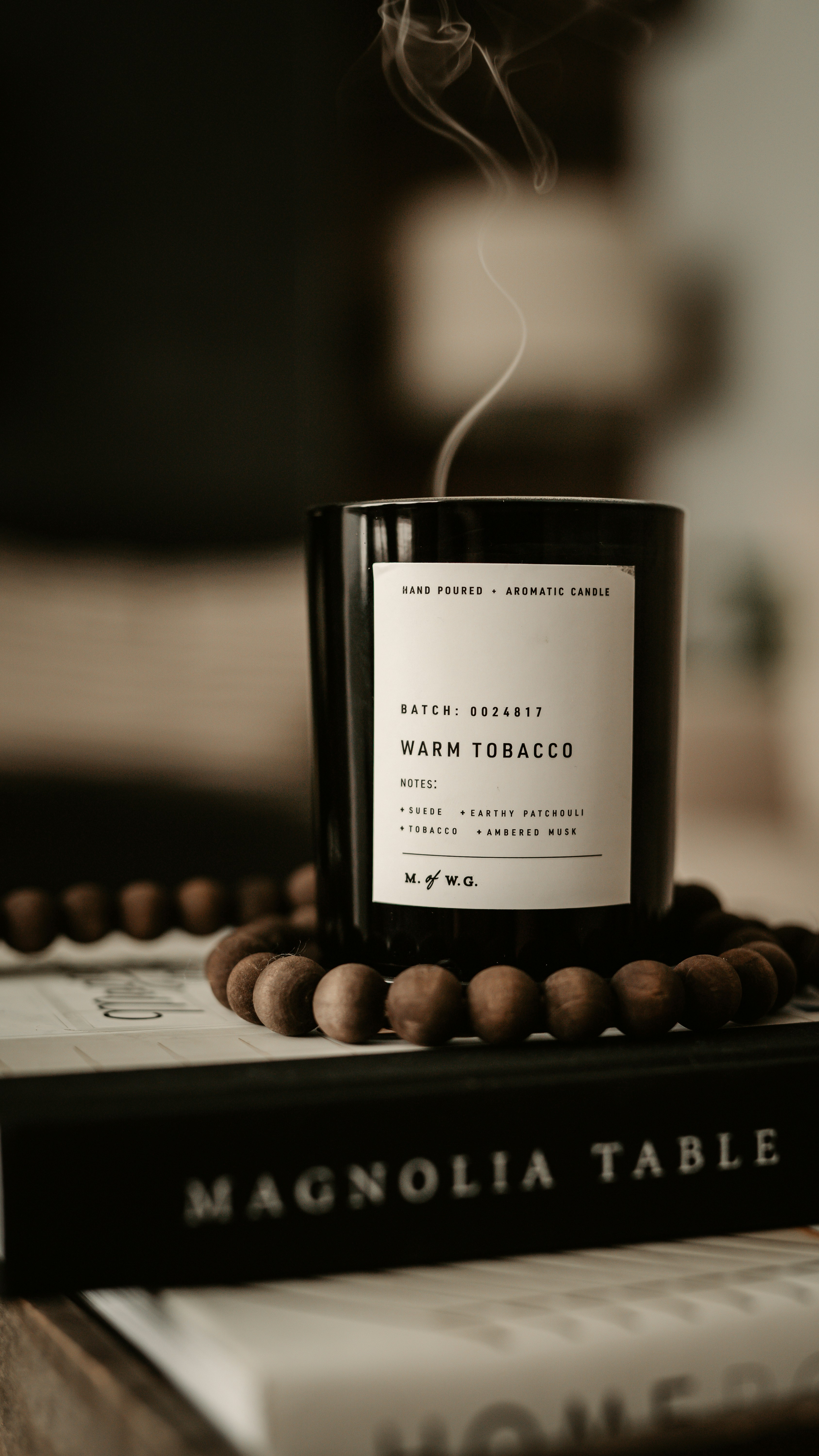 Warm Tobacco Candle Nestled Among Wooden Beads and Books