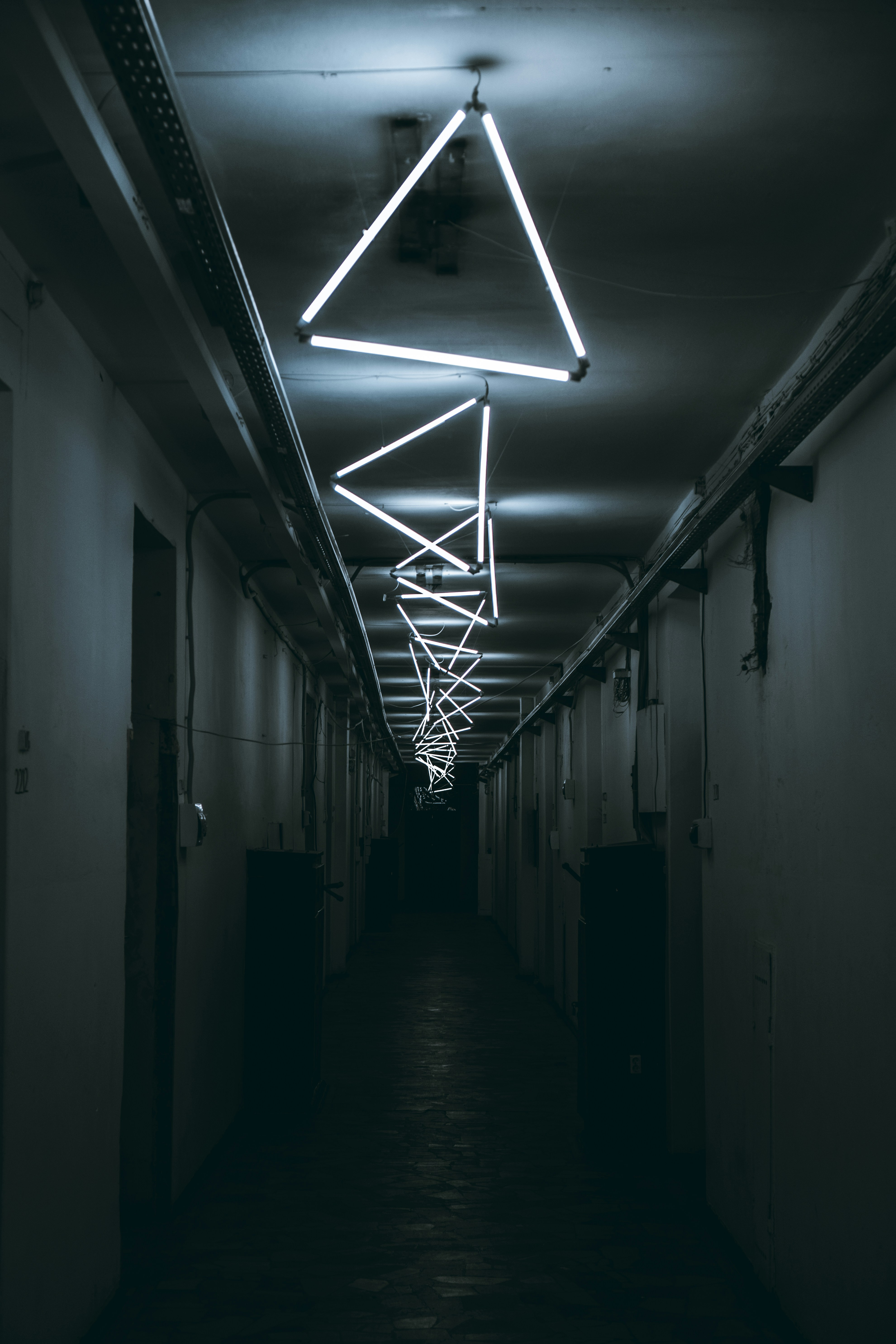 Neon Triangles Etch a Vanishing Point in a Dim Corridor