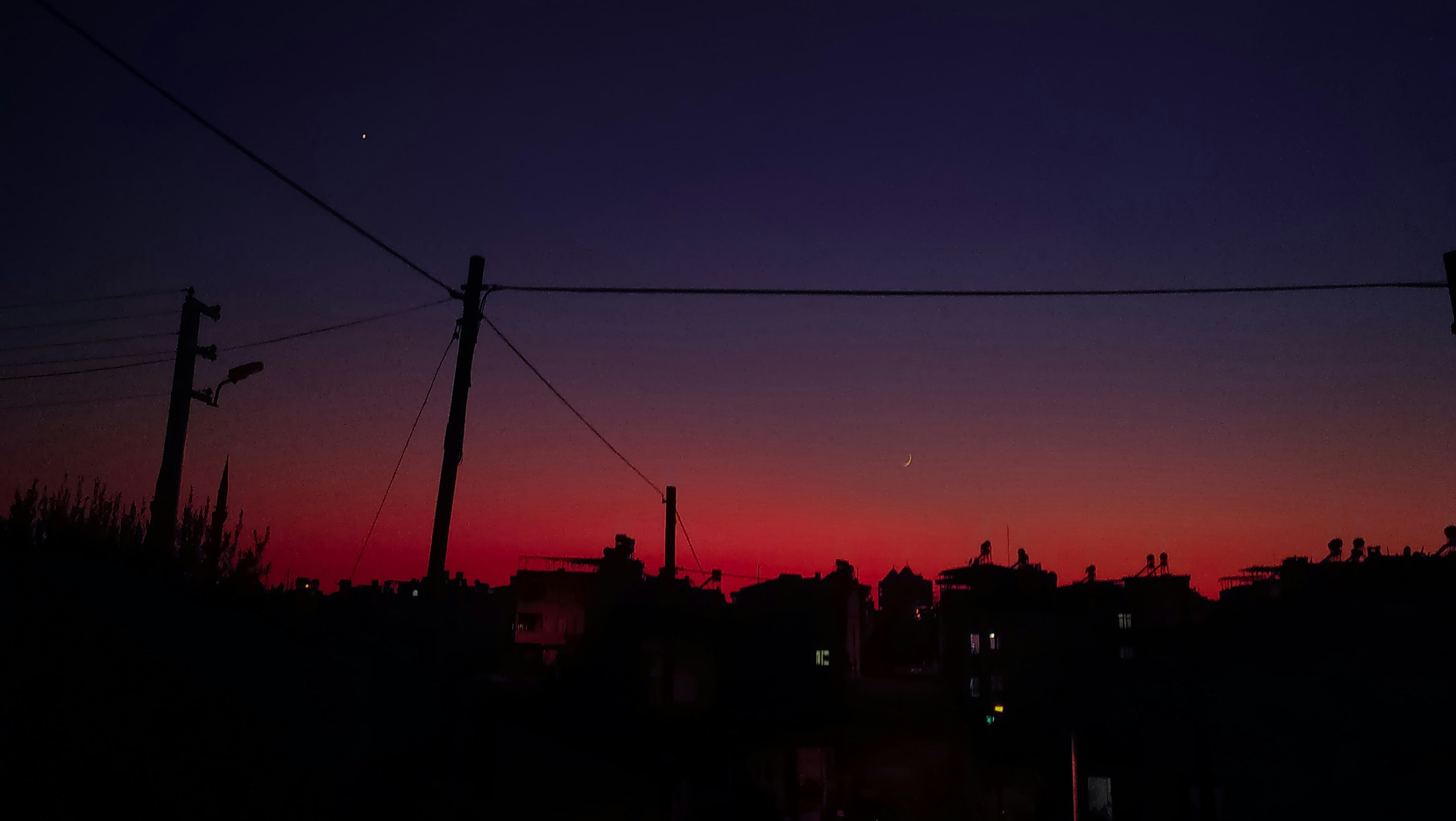 Deep twilight sky with vibrant red and purple hues above a silhouetted cityscape and power lines.
