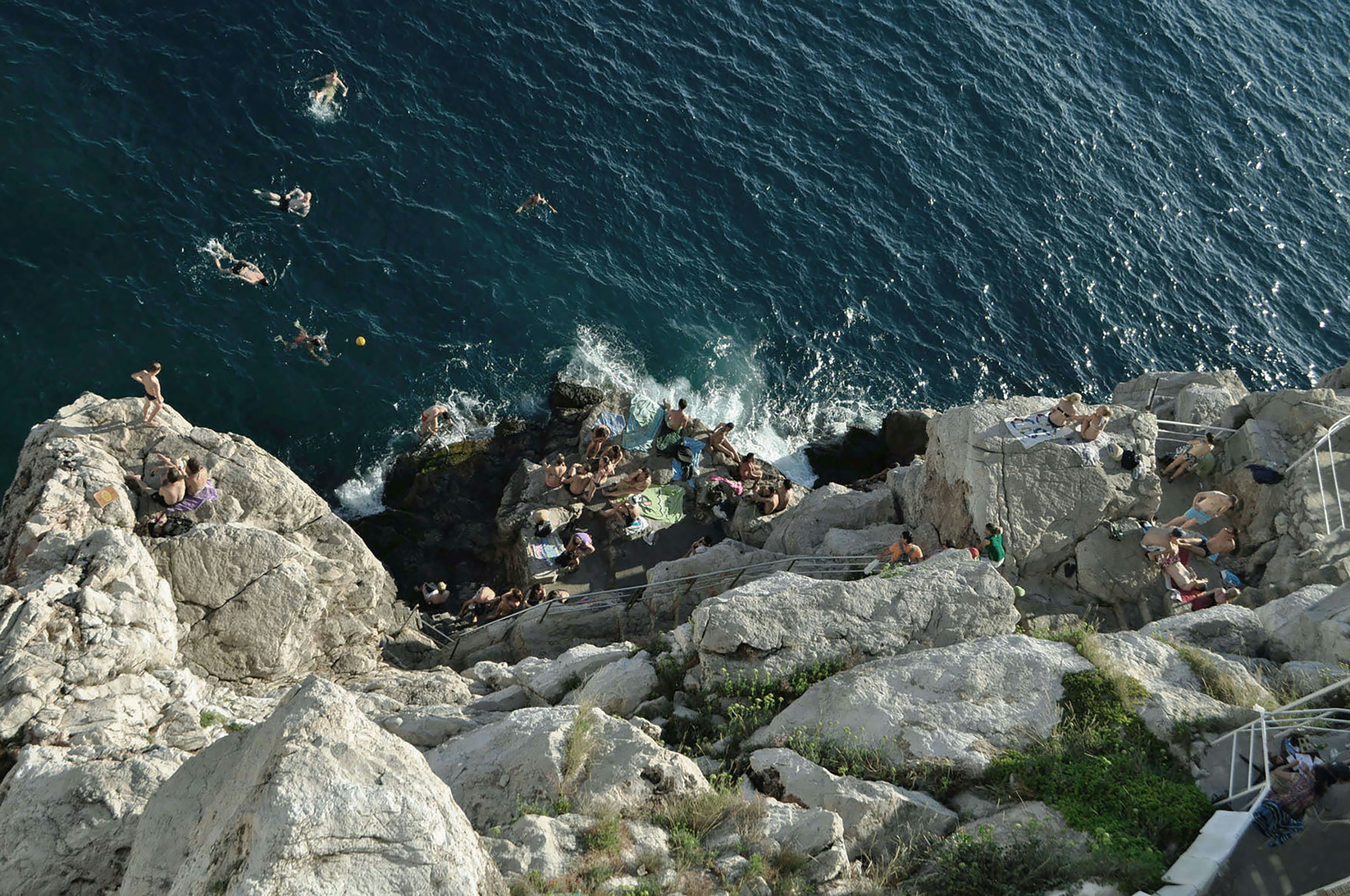 Cliffside Gathering: Sunlit Figures Among Jagged Rocks and Sea Spray