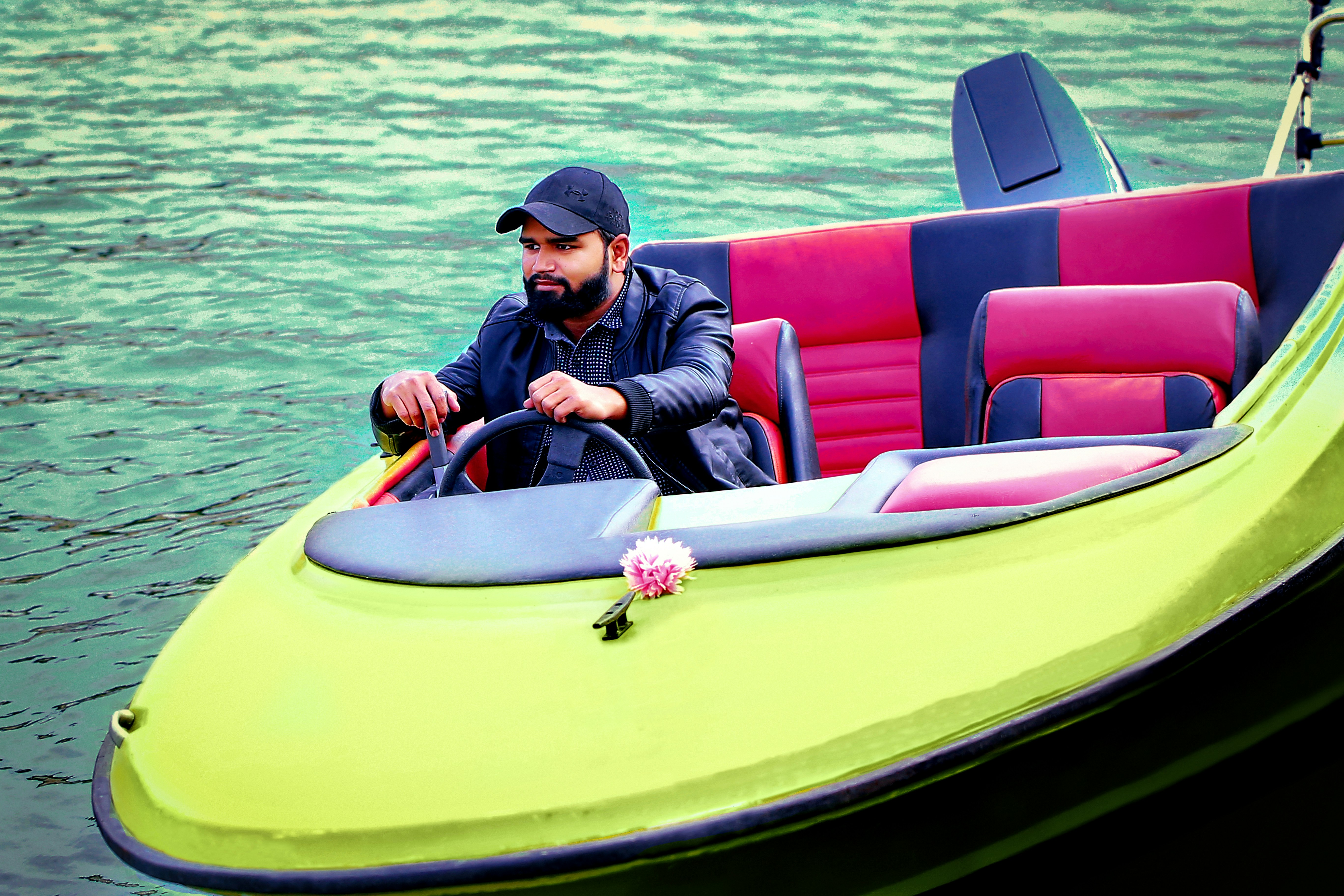 Man in a bright green and red speedboat navigating clear, green waters.