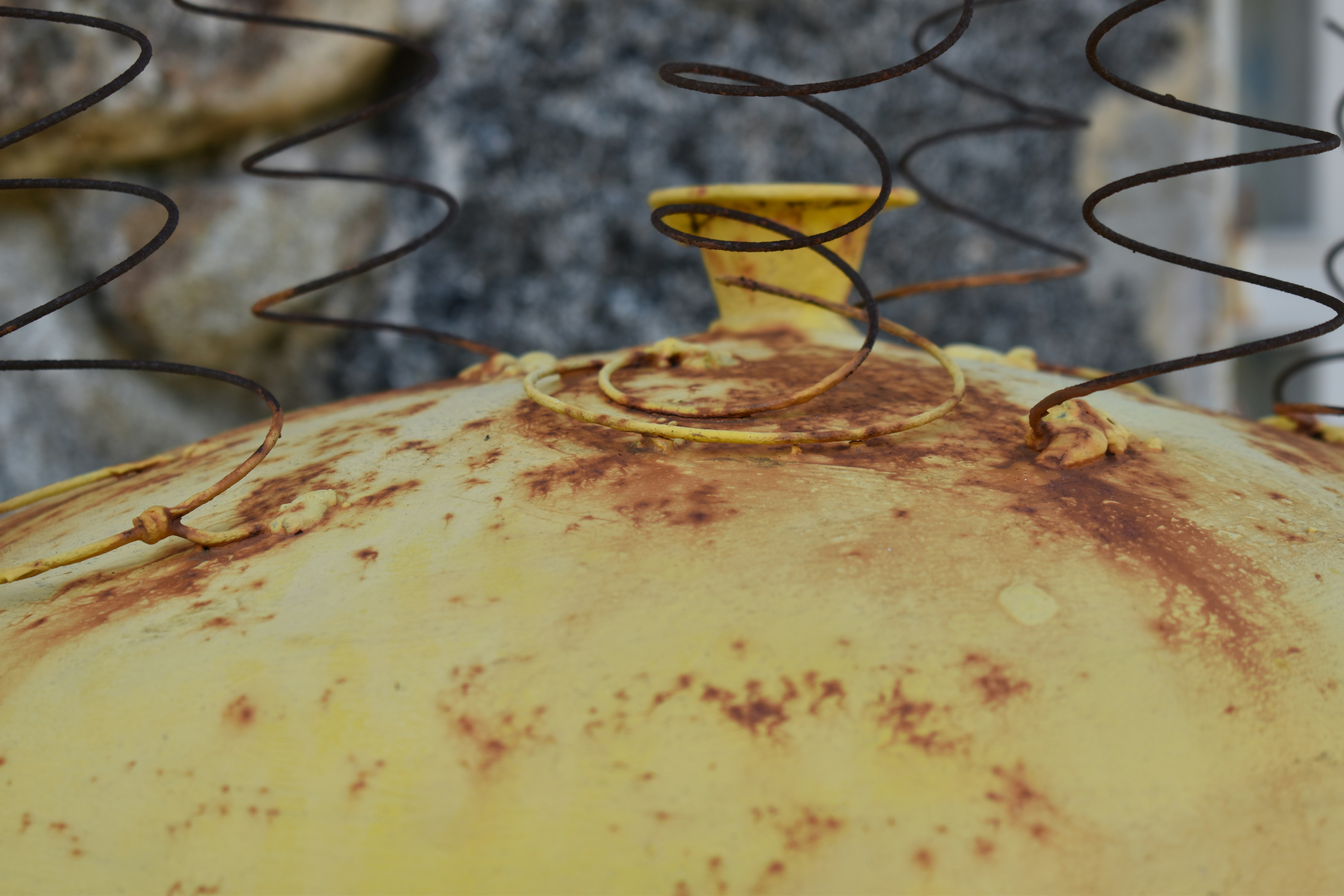 Crown of Rust: Close-Up on a Weathered Yellow Lid Entangled by Wires