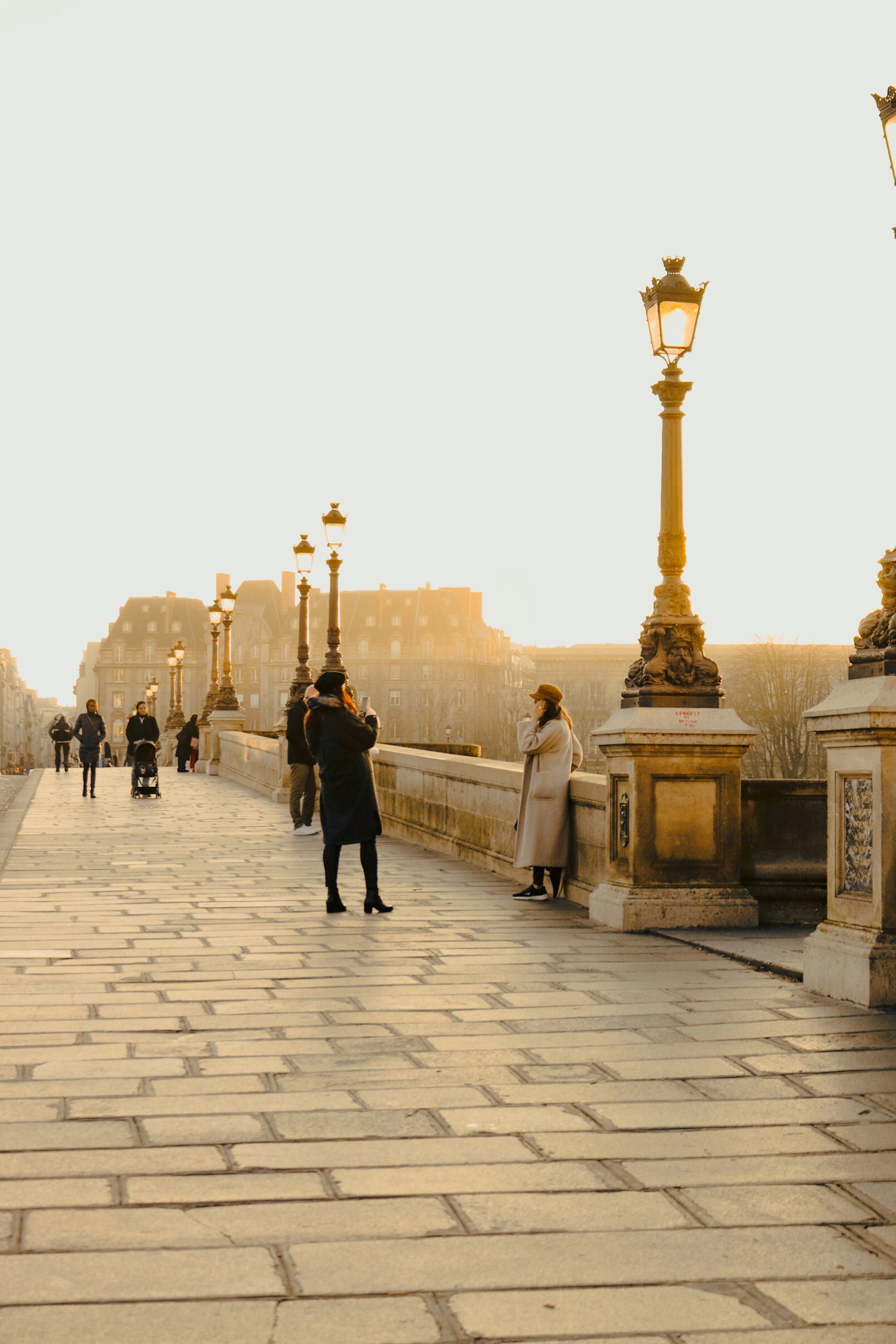 A group of people walking on a stone walkway with tall gold statues ...