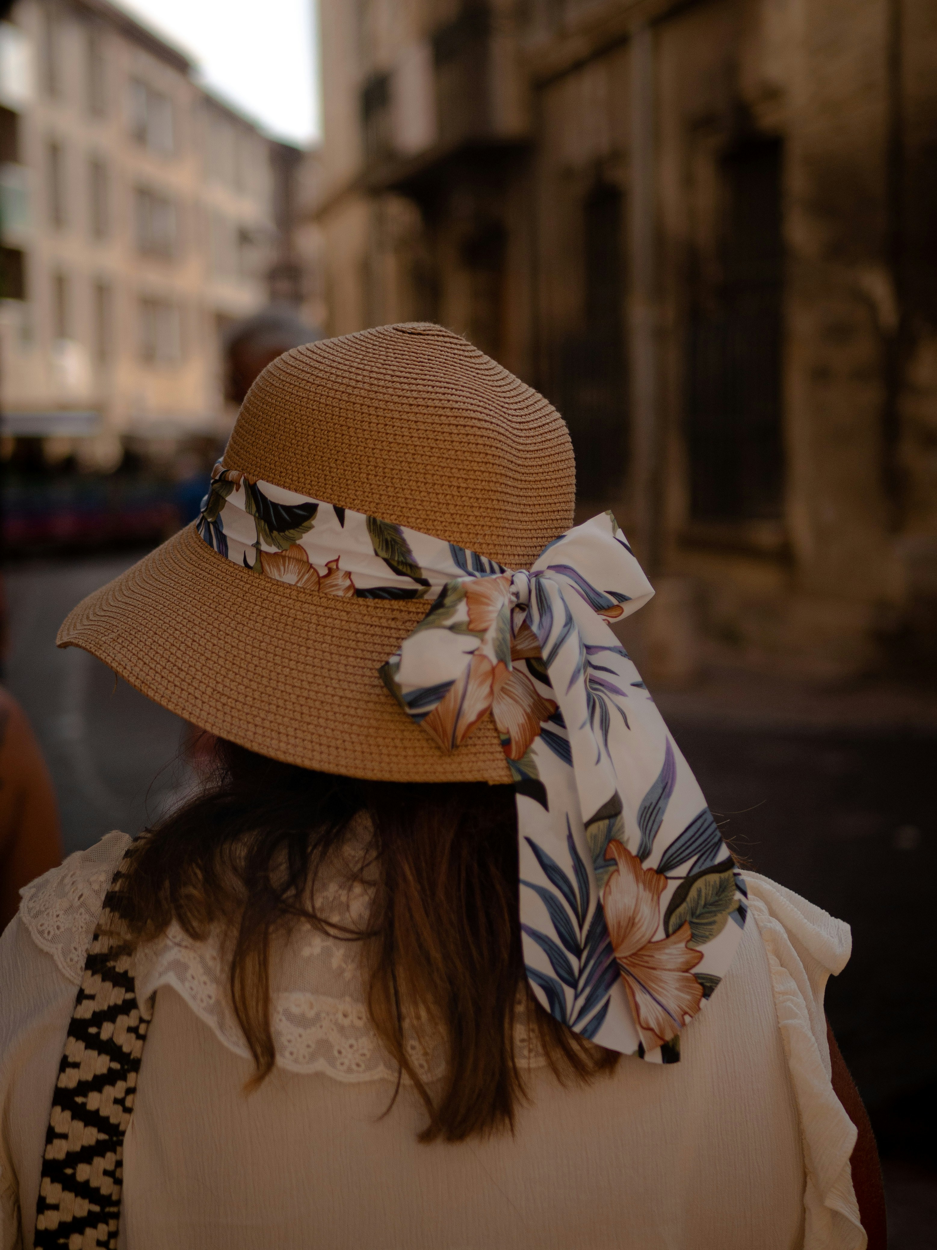 Woman in a floral-brimmed hat walking down a shadowed street in soft evening light.