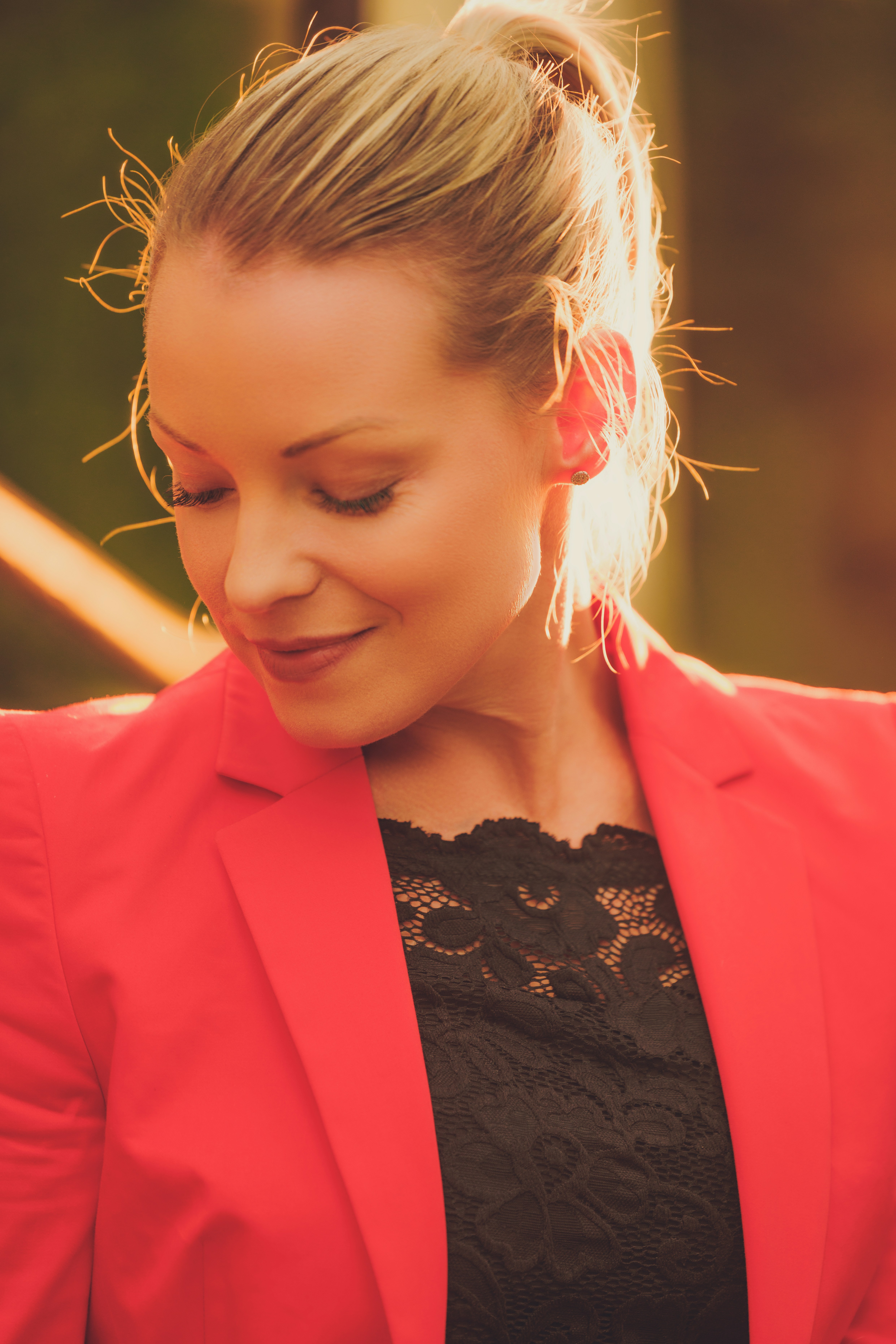Portrait of a woman in a coral blazer with black lace top, softly backlit by warm sunset light.