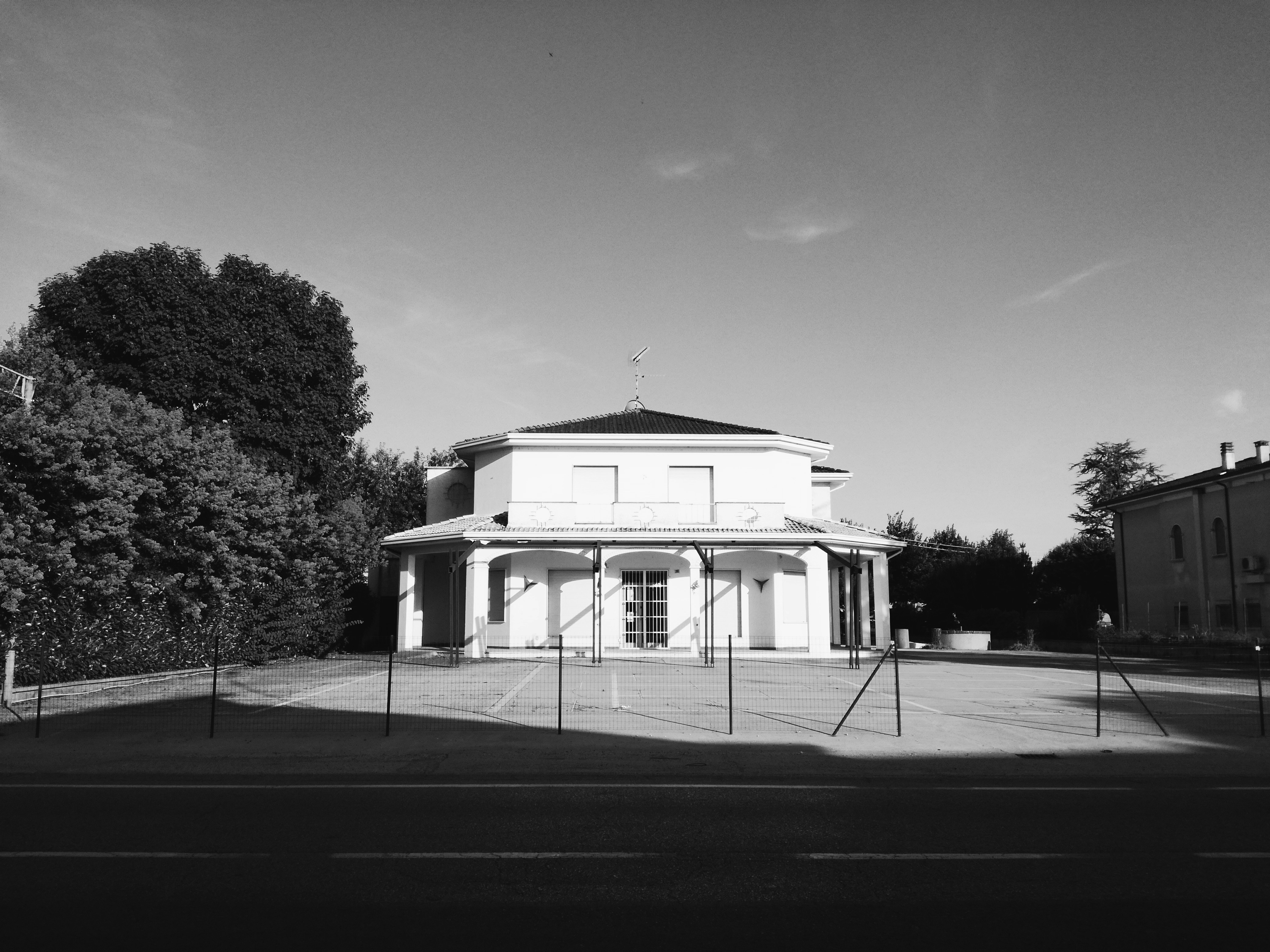 Grayscale photograph of a neoclassical pavilion framed by trees and an empty forecourt, emphasizing symmetry and open space.