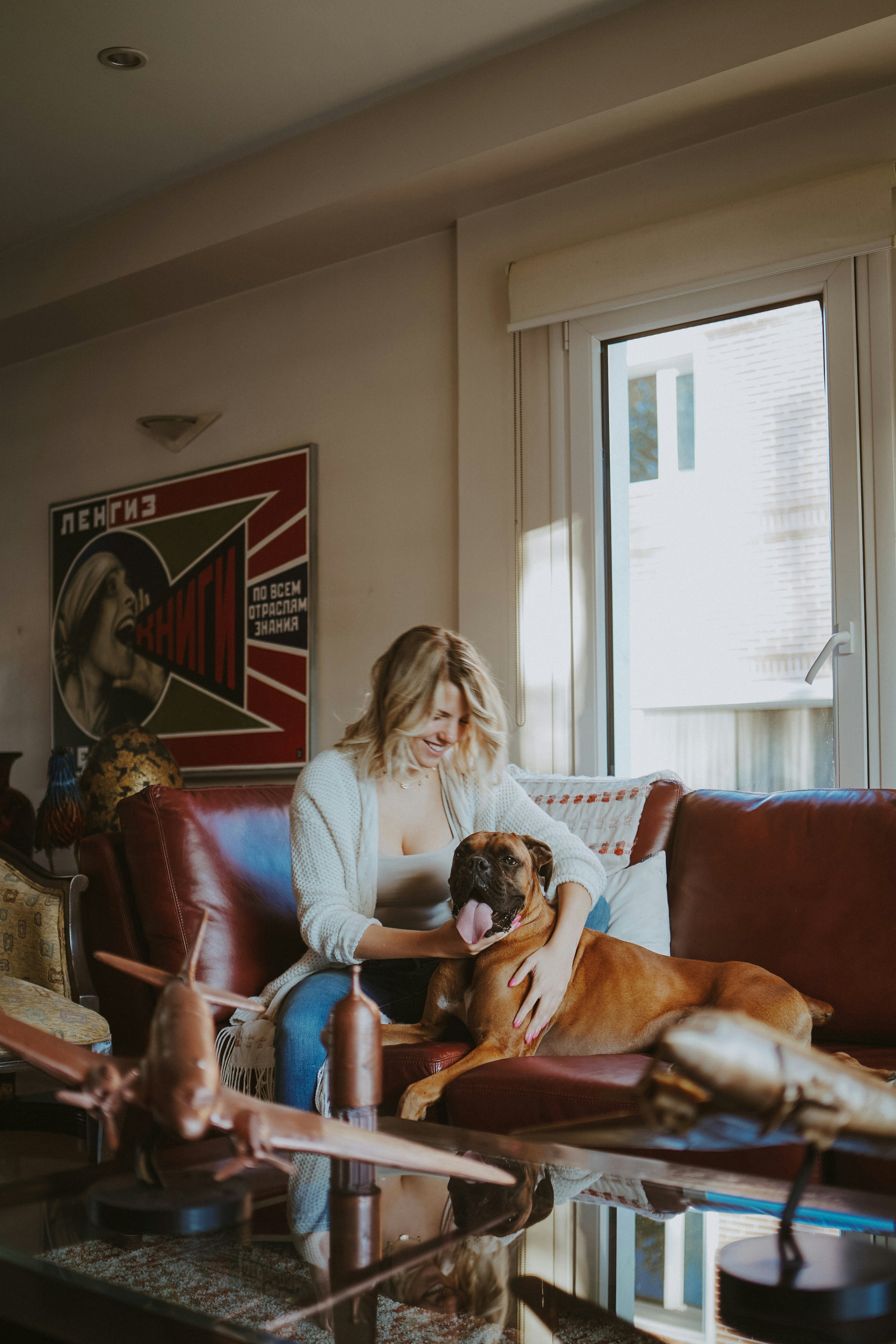 A woman gently interacts with her playful dog on a cozy sofa, surrounded by eclectic decor. The warm ambiance highlights their affectionate connection.