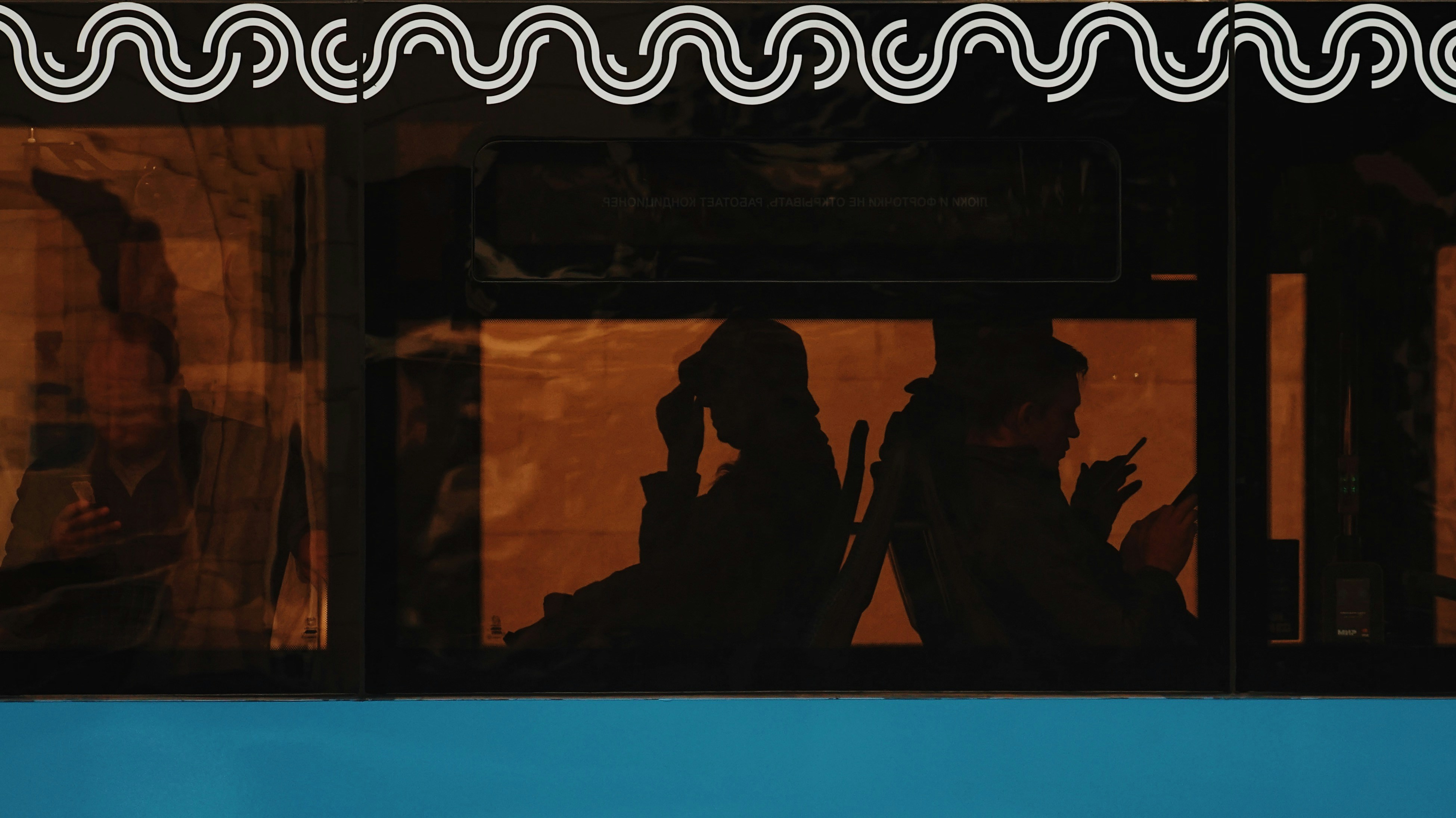 Silhouetted passengers inside a tinted bus window at dusk