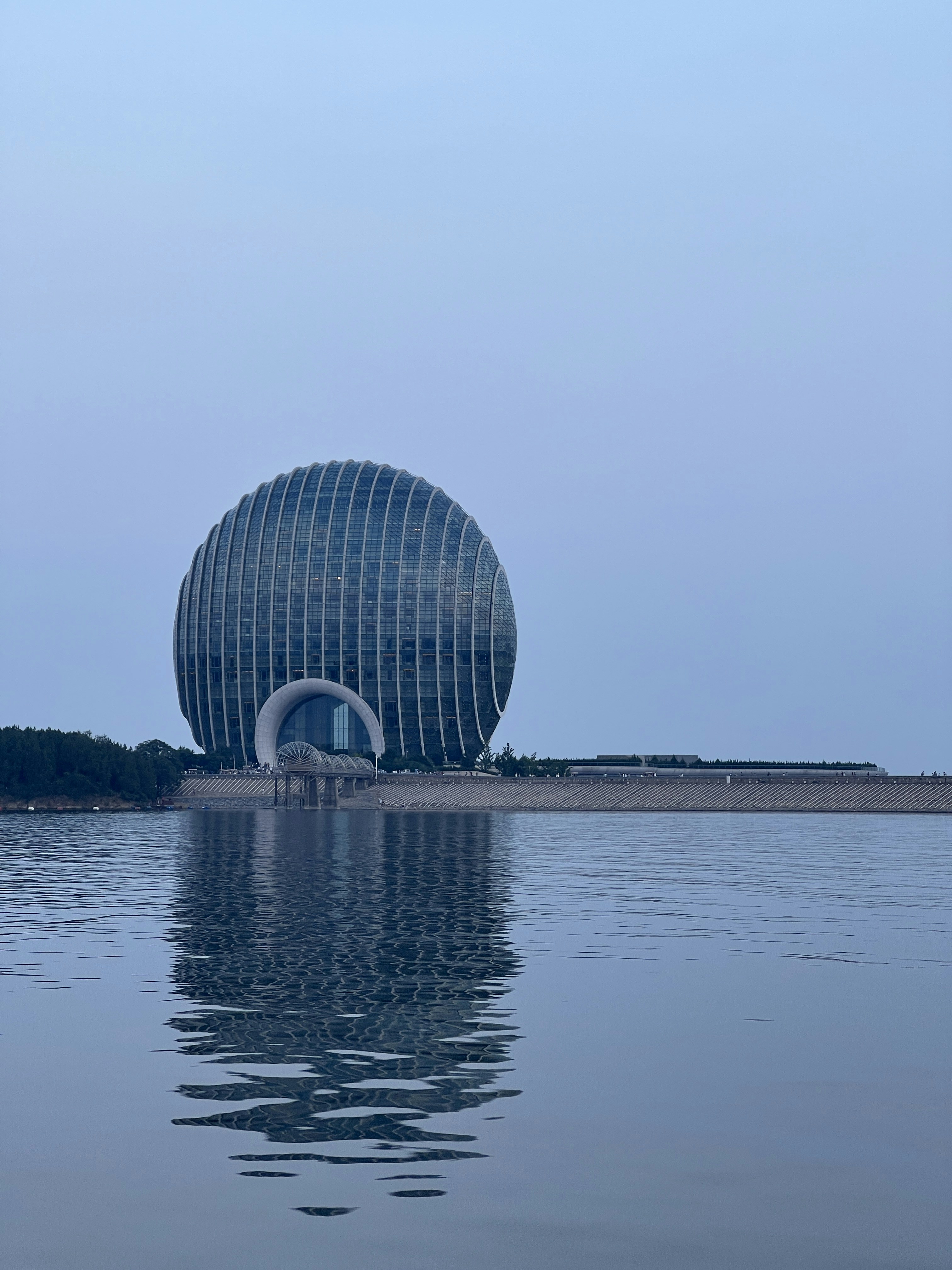 A contemporary building resembling a large sphere, reflecting in still waters, surrounded by serene landscapes.