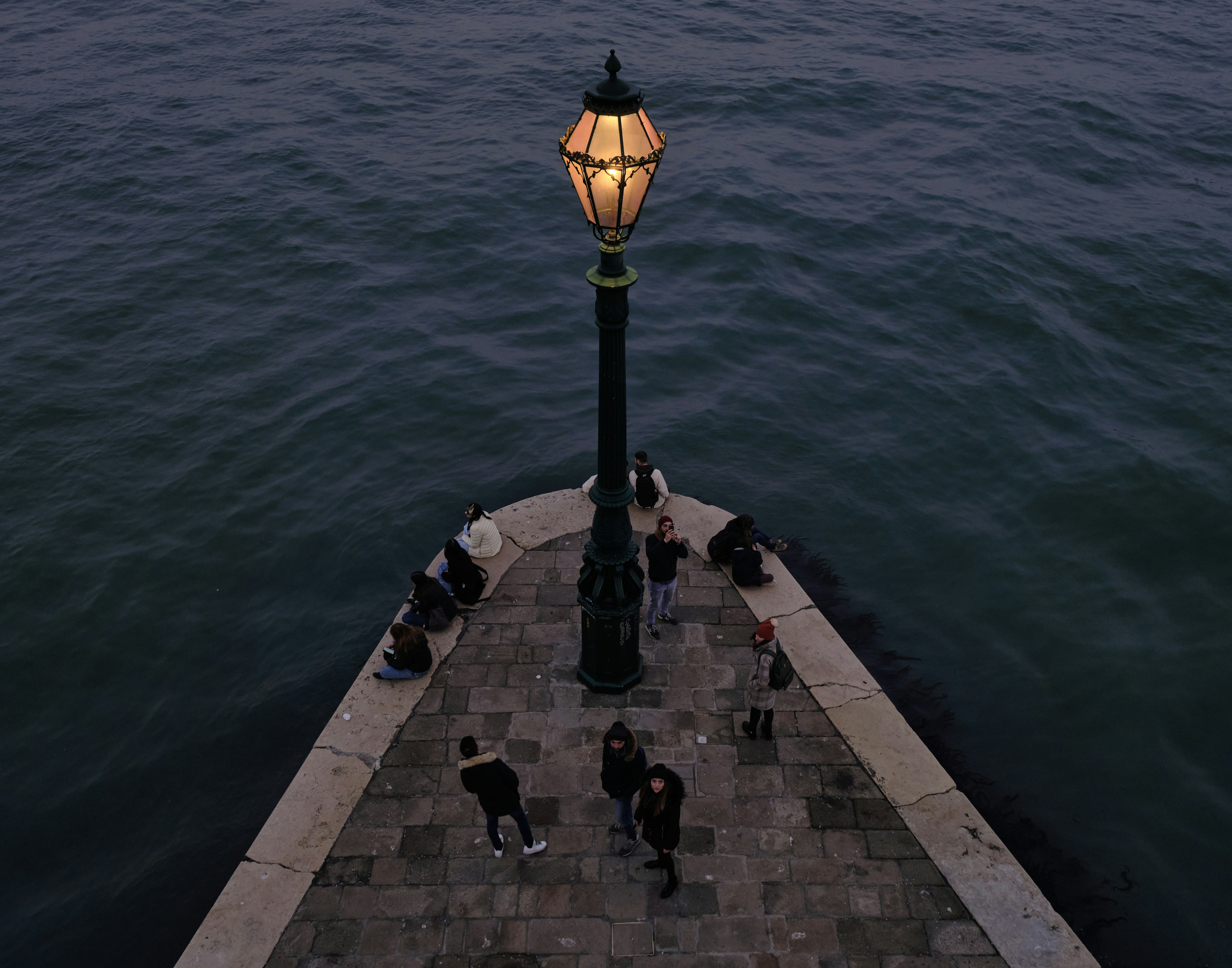 A group of people sitting on a stone walkway over water photo – Free ...
