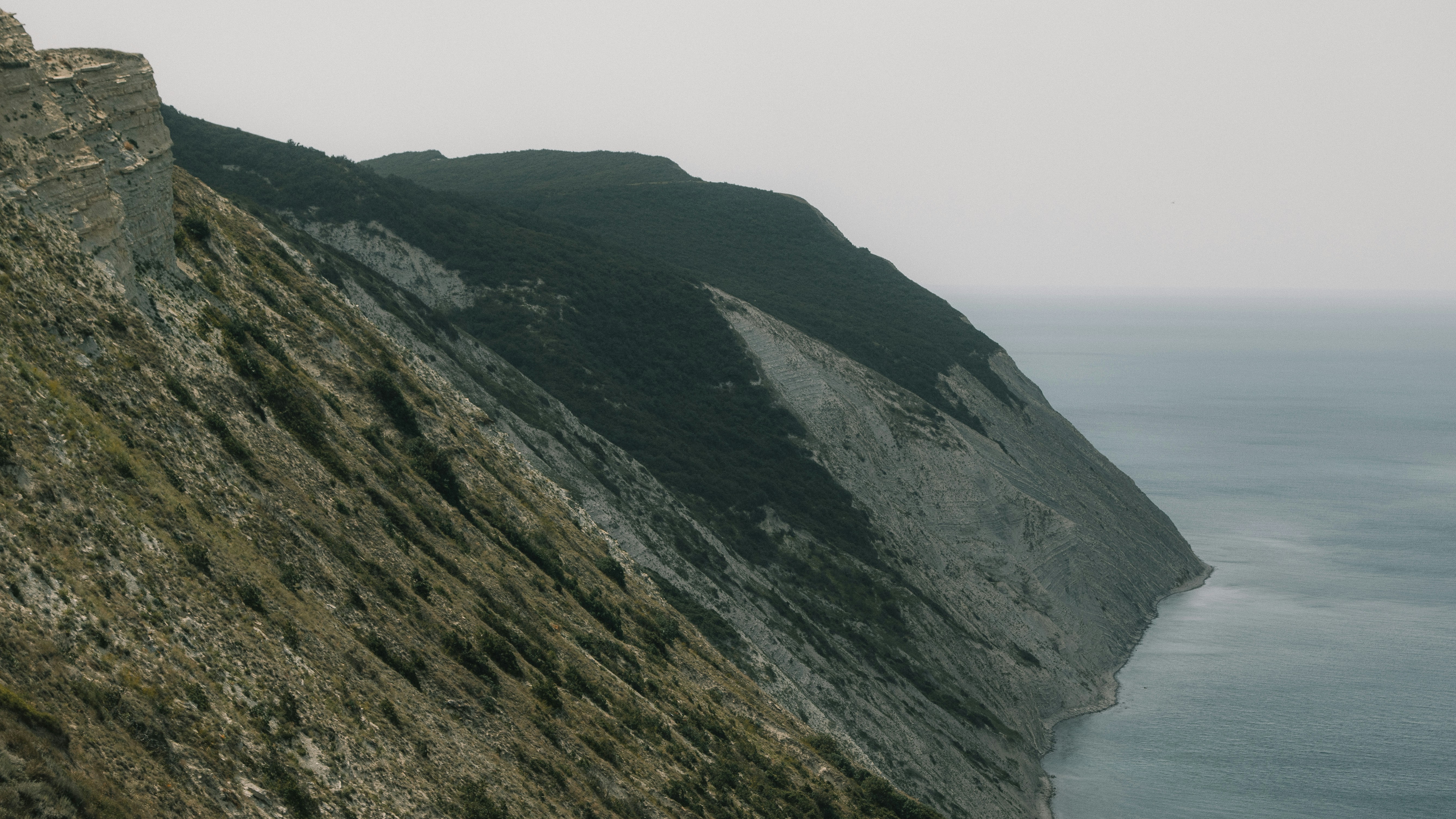 A rugged coastal cliffside meets the tranquil sea, showcasing the stark contrast between earth and water. The muted colors evoke a sense of calm and solitude.