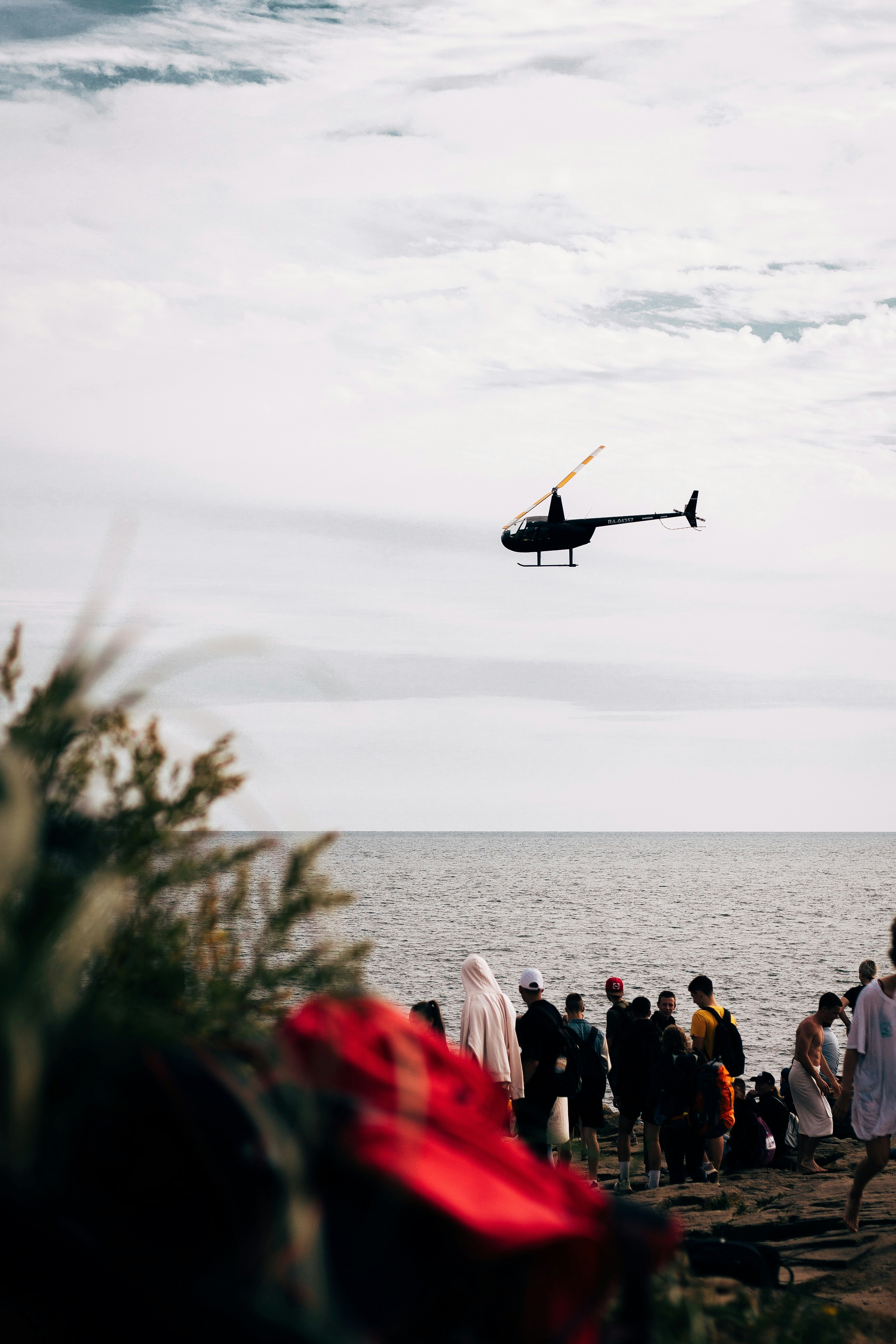 Shoreline Rendezvous: Helicopter Hover Above a Crowd by the Sea