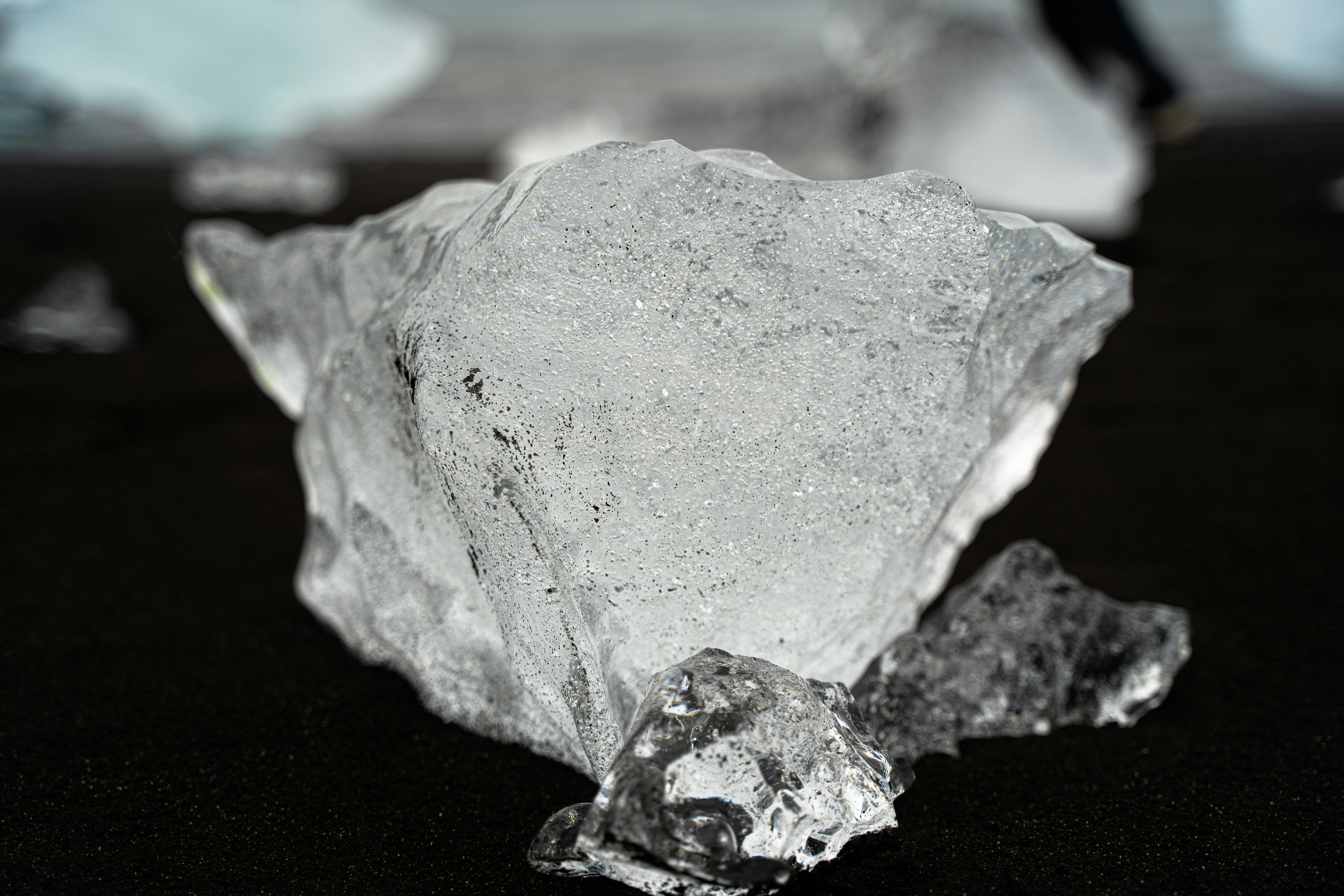 Chunk of glacial ice resting on black volcanic sand, showcasing intricate textures and reflections under soft lighting.