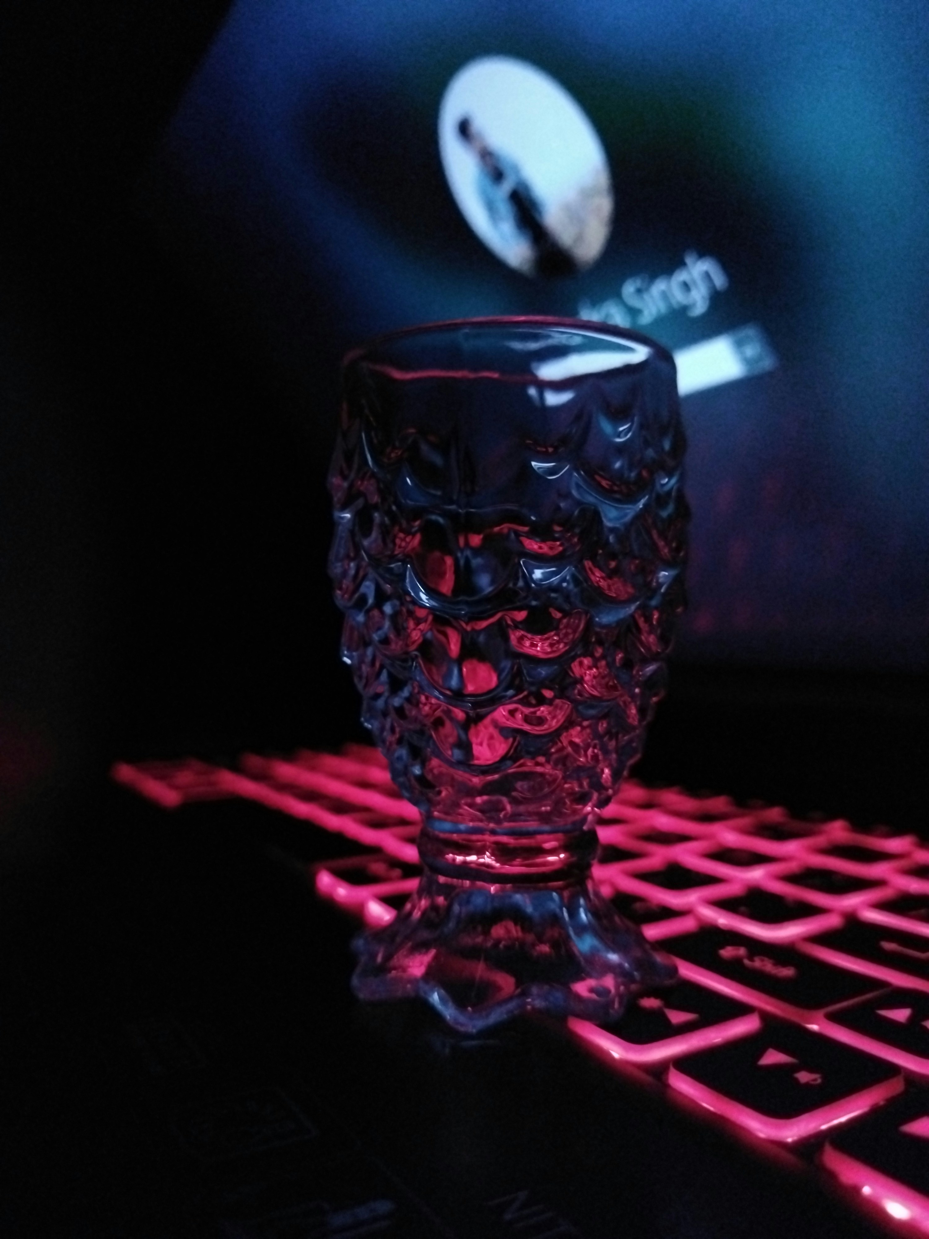 Textured crystal glass sits on a pink-lit keyboard with a blurred blue laptop screen glowing in the background.
