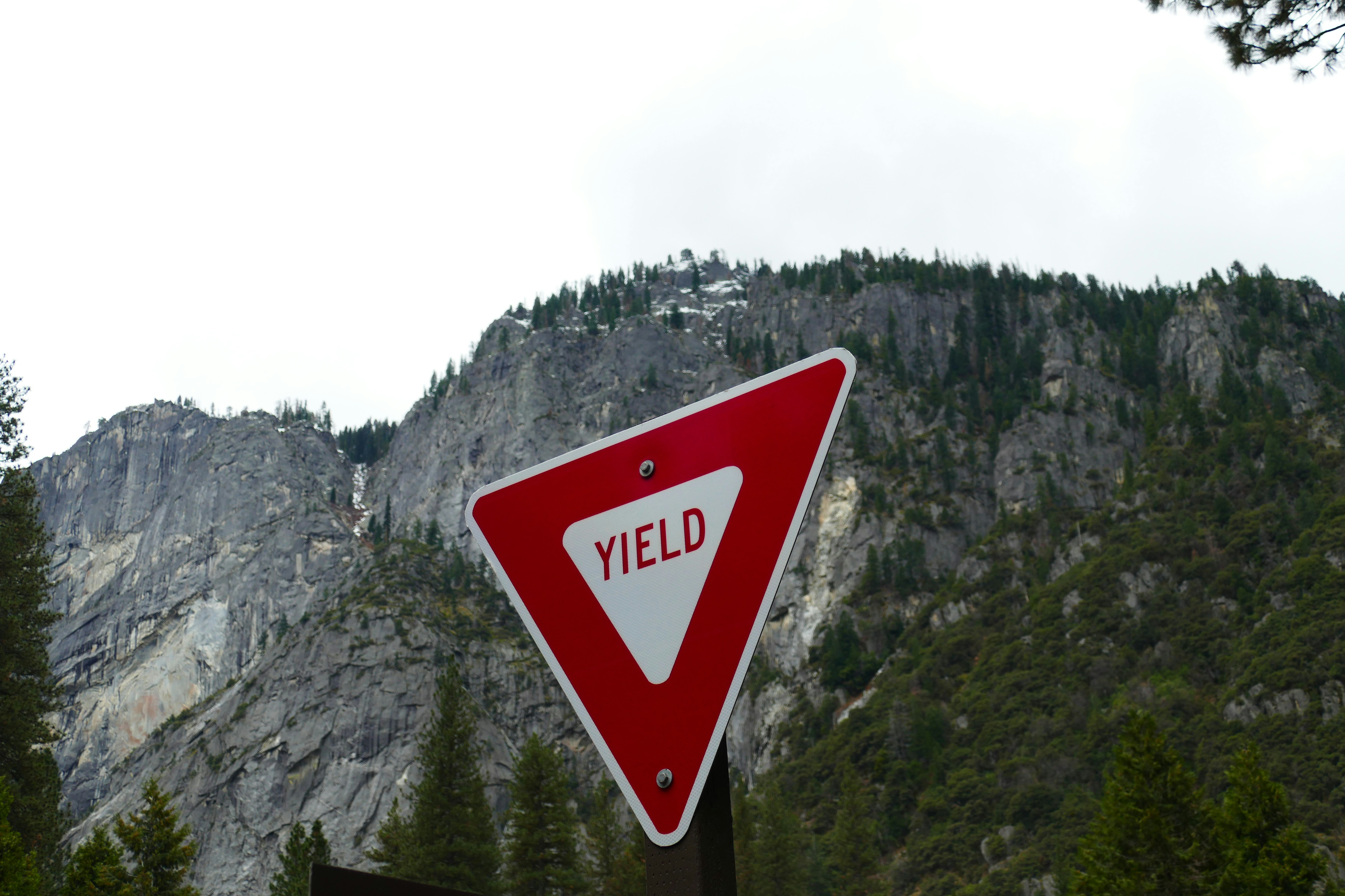 Yield sign prominently displayed in a mountainous landscape, surrounded by towering cliffs and lush trees.