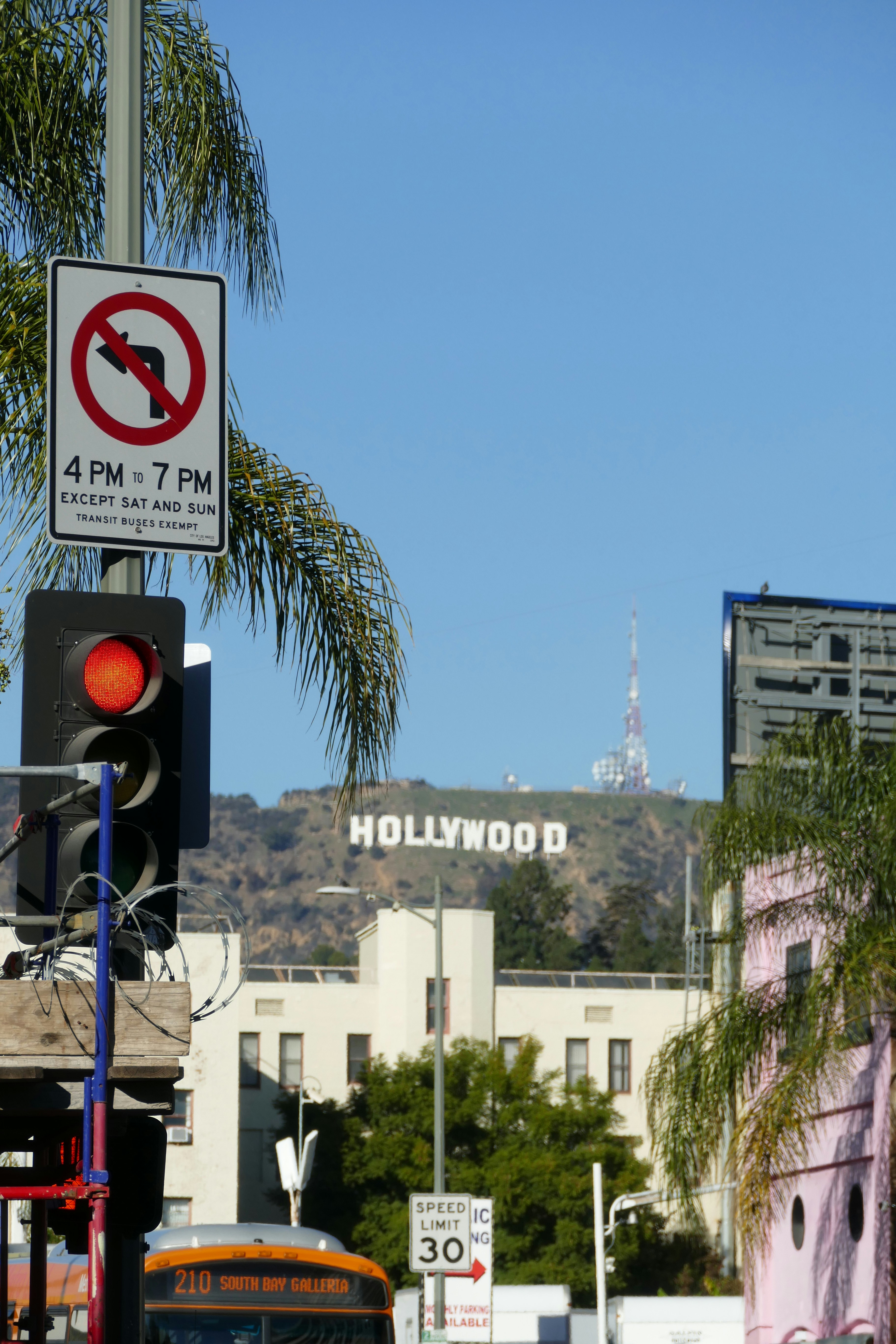Hollywood sign framed by urban elements, including traffic signals and palm trees, showcasing the blend of city life and iconic landmarks.