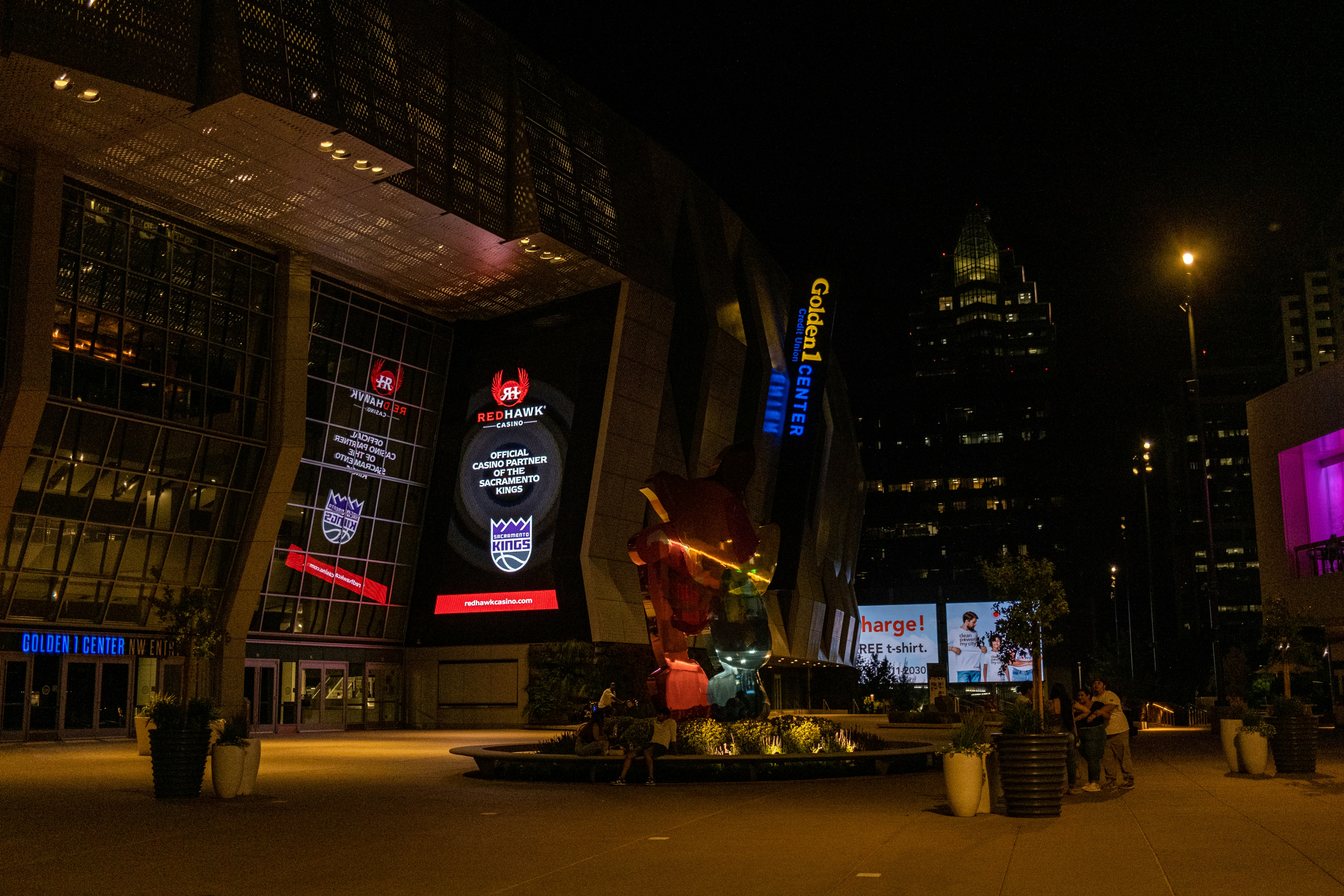 Neon Sentinel in the Night Plaza: A Colorful Sculpture Framed by Digital Windows