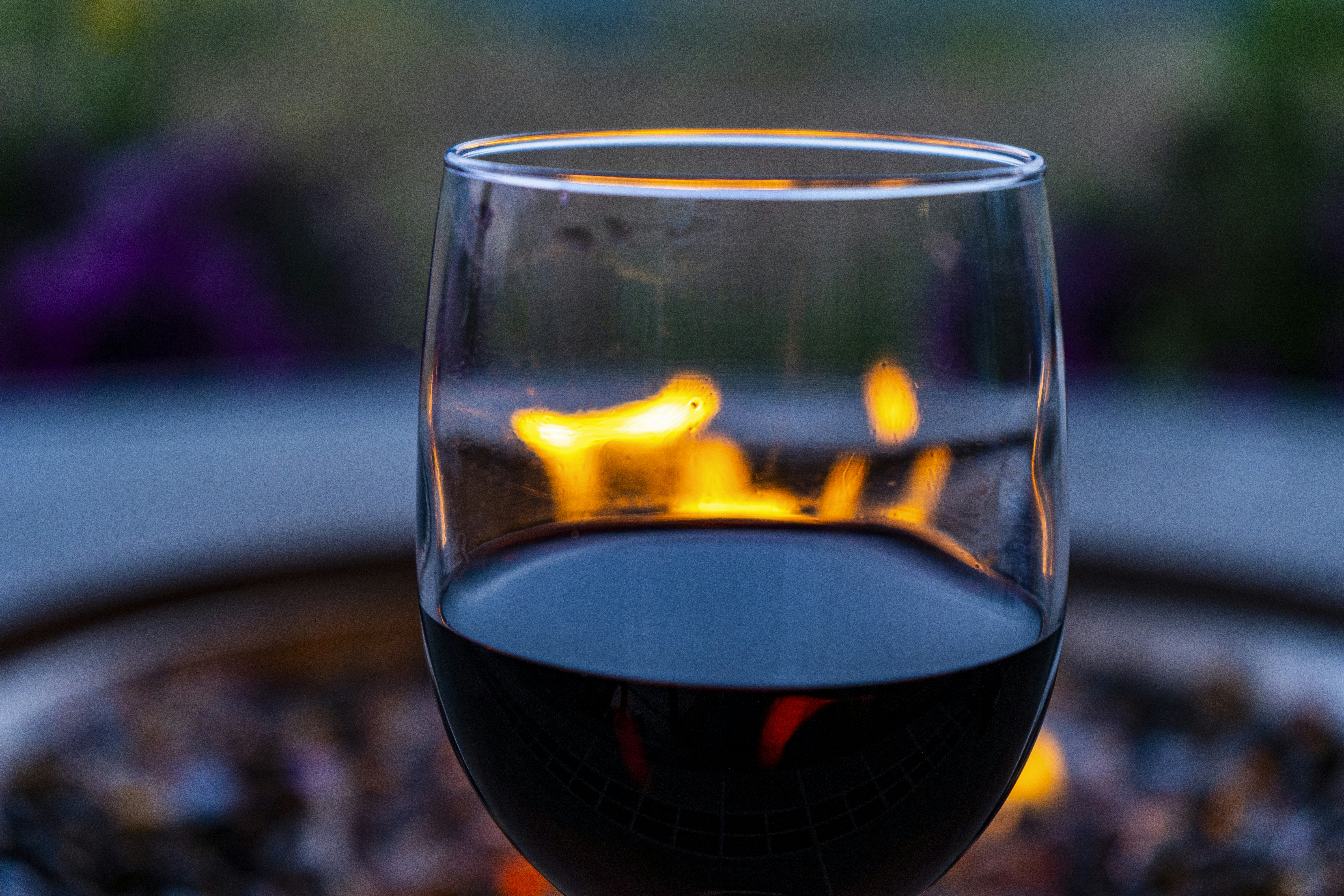 Glass of red wine in front of a flickering fire pit at dusk.