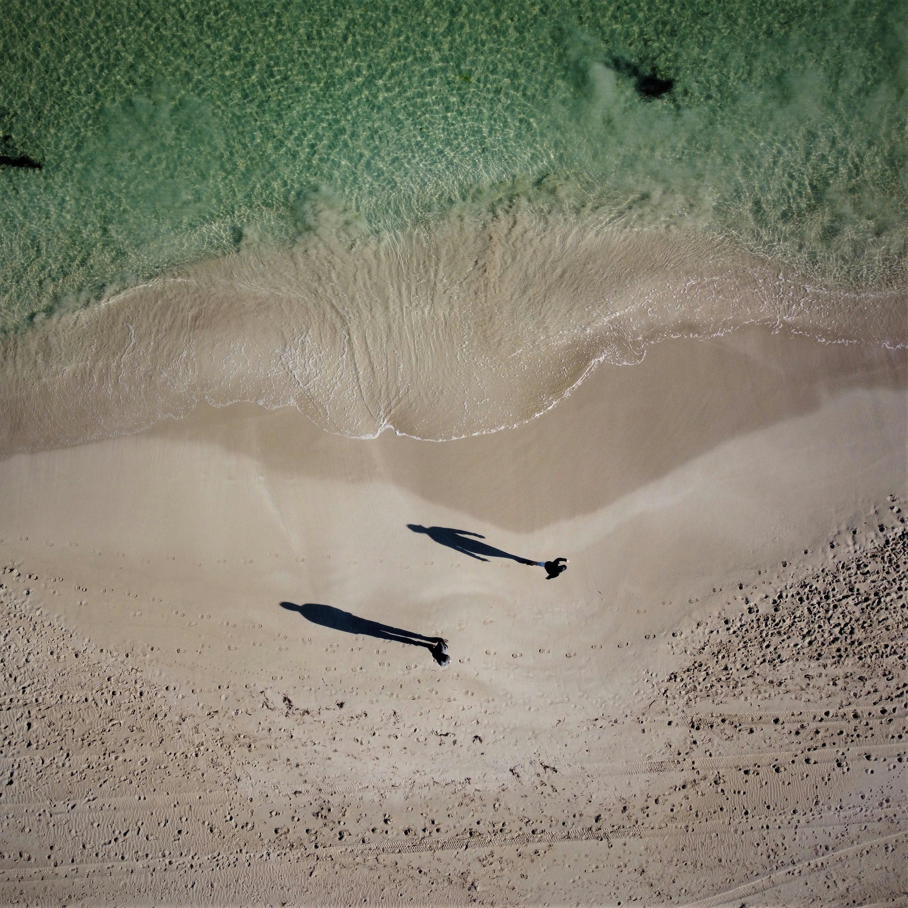 Two Beachgoers Cast Long Shadows on a Turquoise Shore