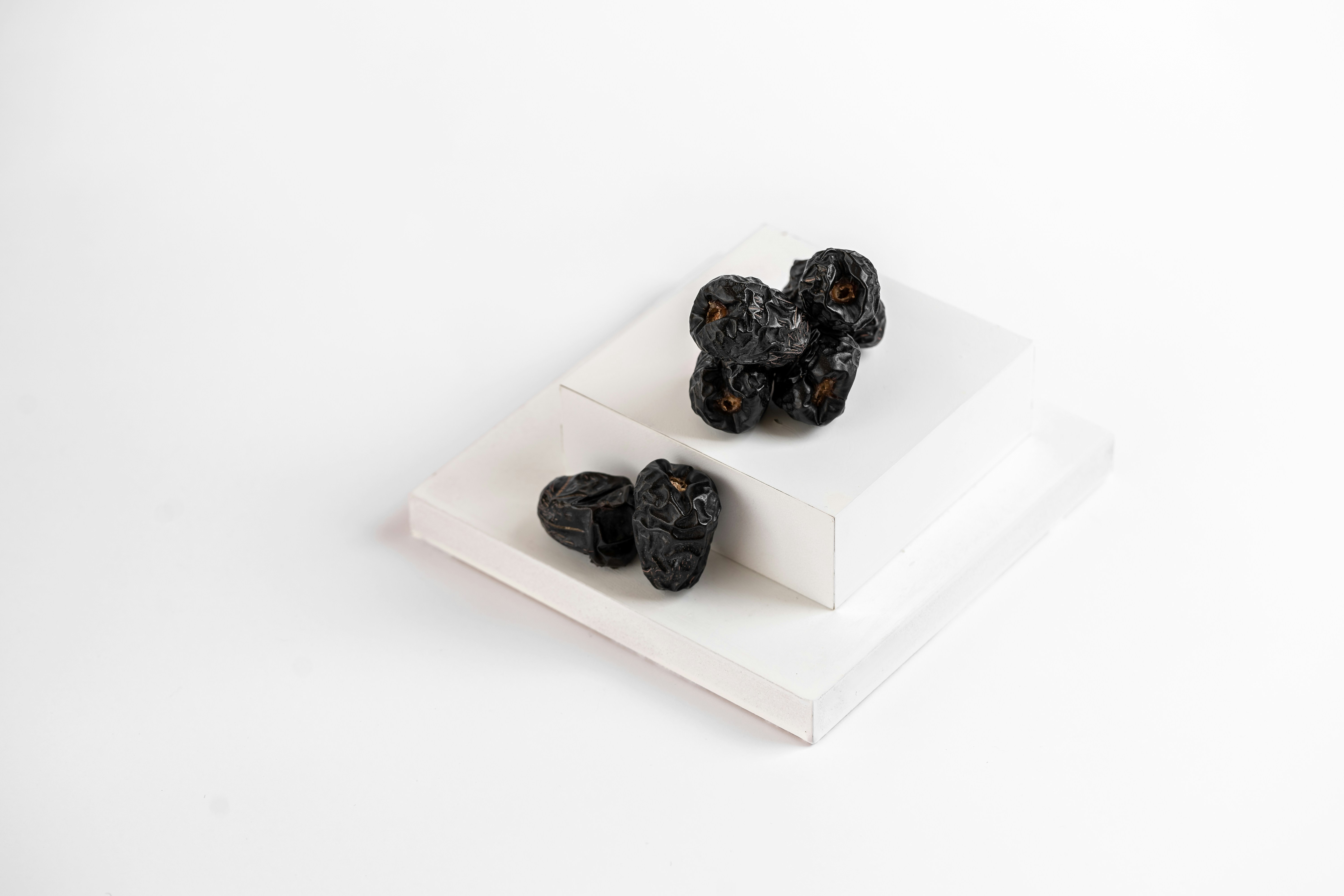 Dried fruits arranged artistically on white geometric platforms, showcasing their rich texture against a minimalist background.