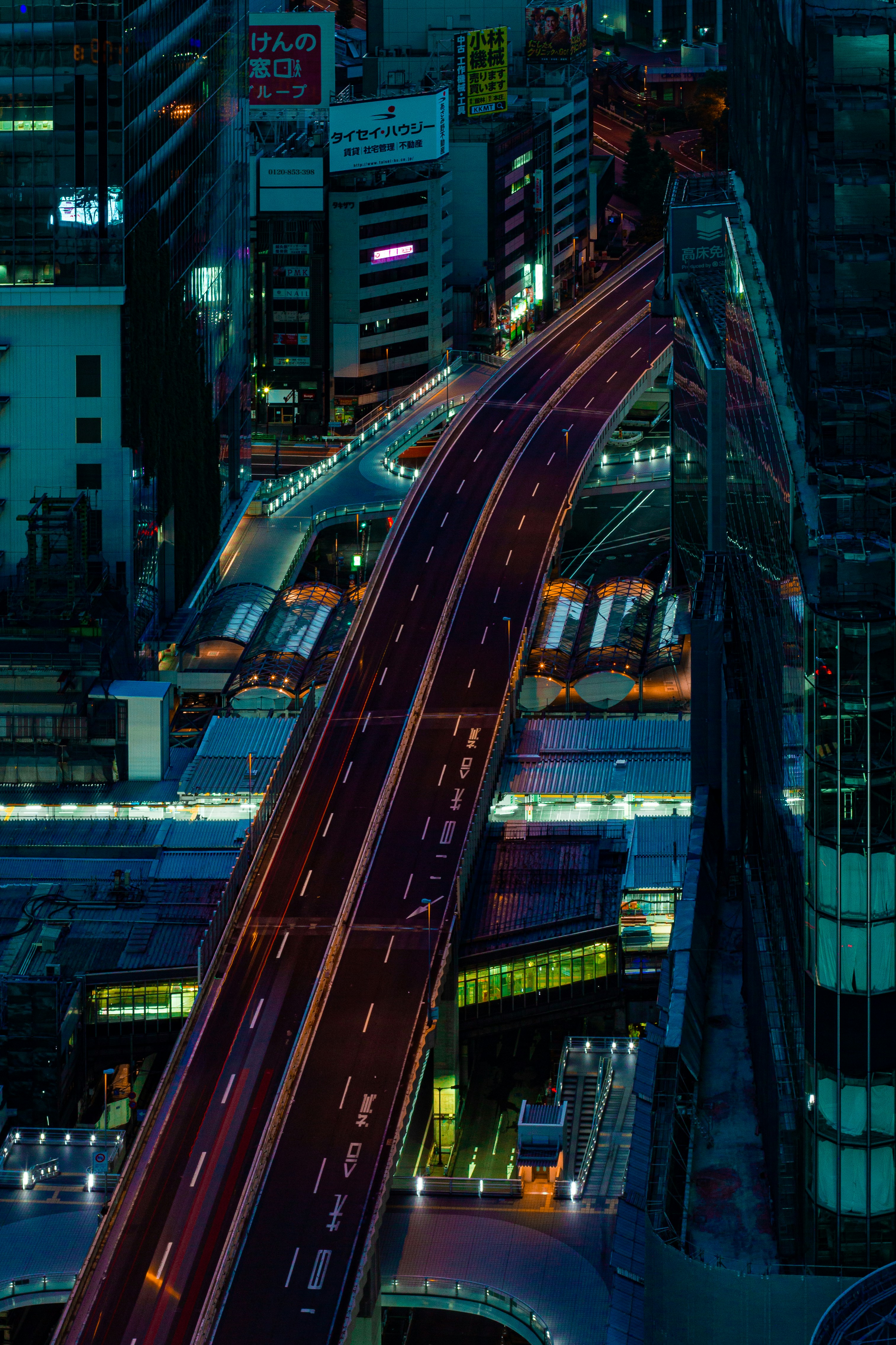Aerial view of a winding highway illuminated by city lights, showcasing the dynamic flow of urban transport against a backdrop of towering buildings.