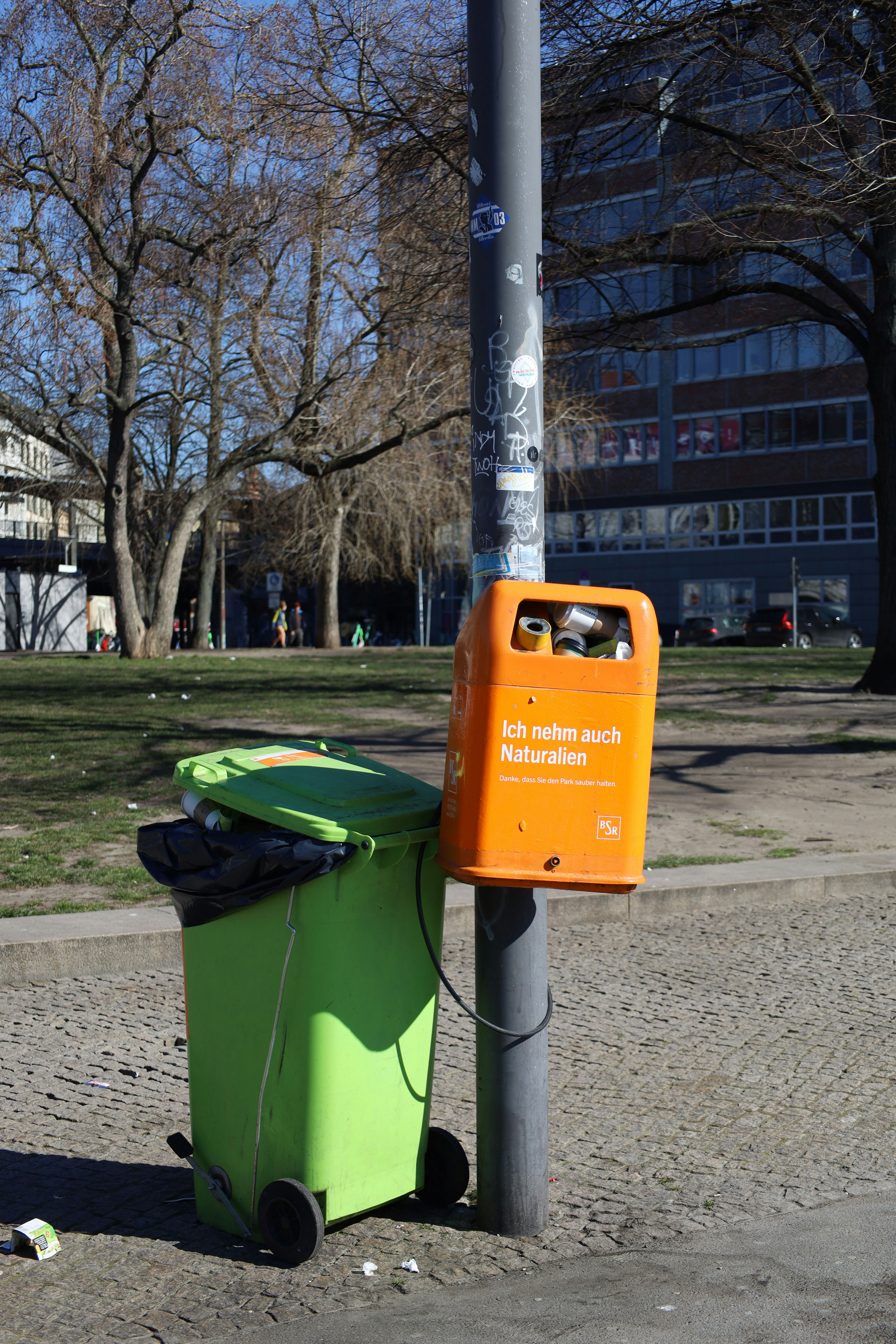 A green trash can next to a pole with a sign on it photo – Free Tin ...