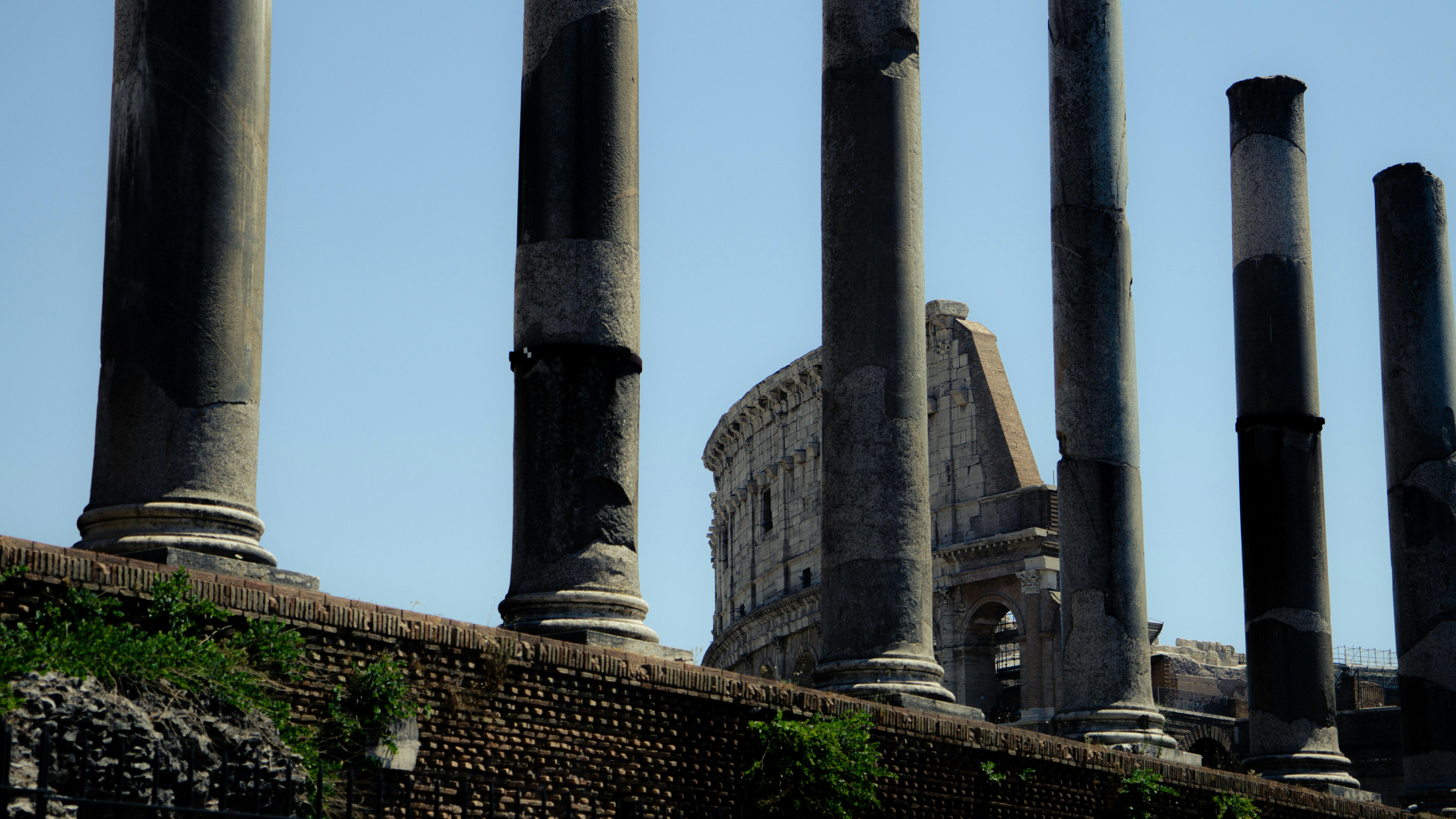 Weathered columns frame the iconic Colosseum, symbolizing the enduring legacy of Roman architecture against a clear blue sky.