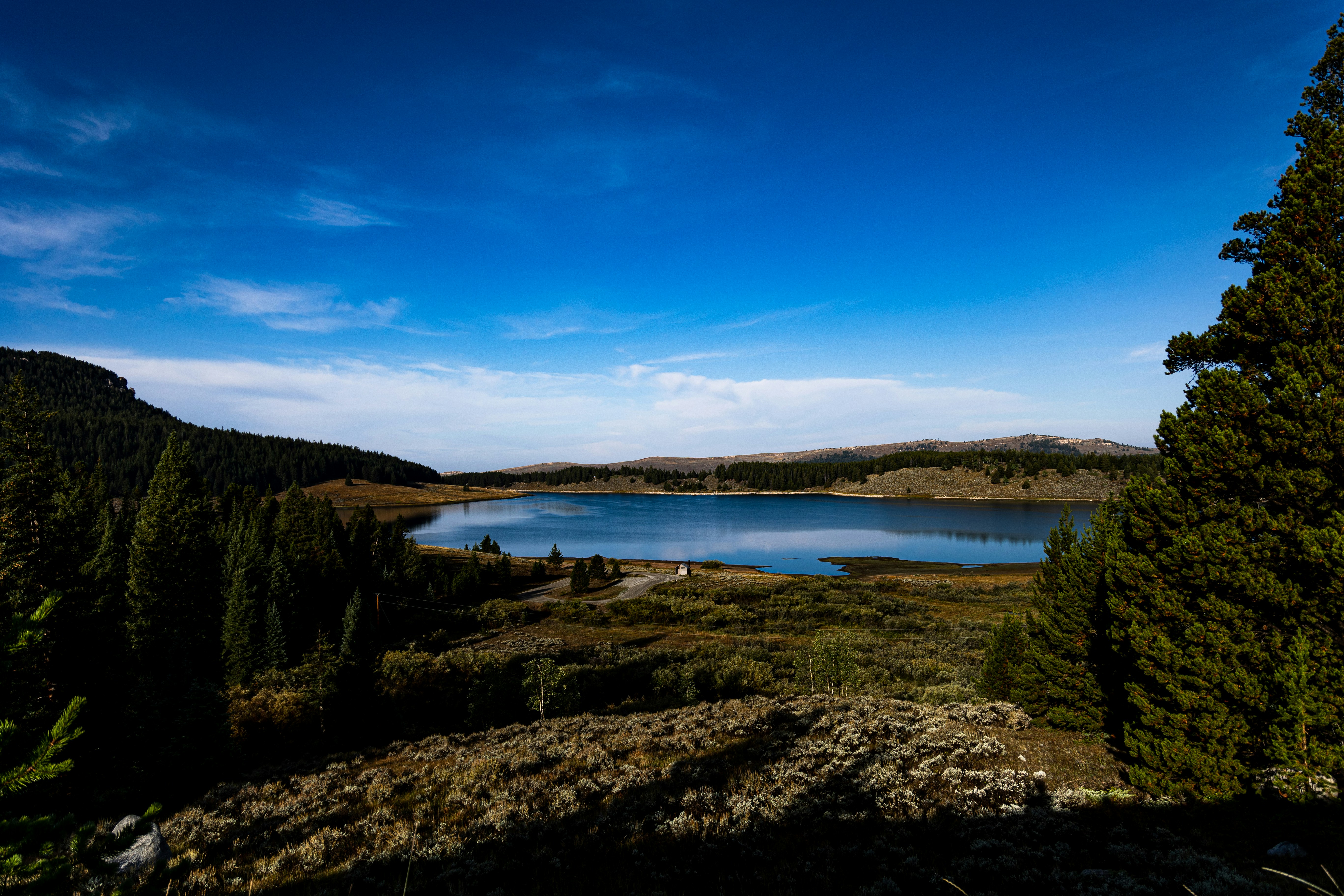 Tranquil mountain lake surrounded by lush greenery under a clear blue sky. A perfect blend of nature's colors and textures.