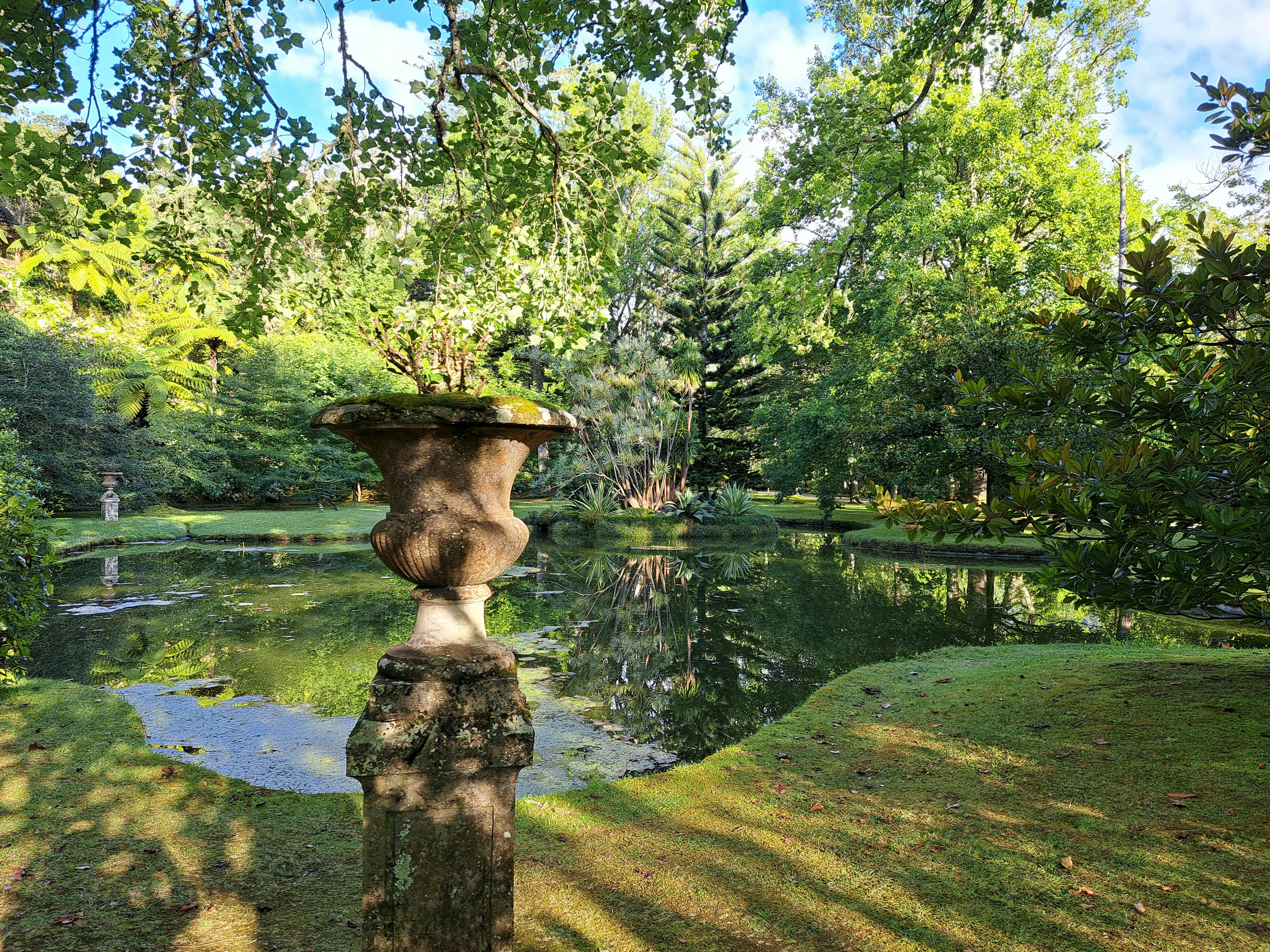 Moss-Covered Pedestal Urn Framed by a Tranquil Garden Pond