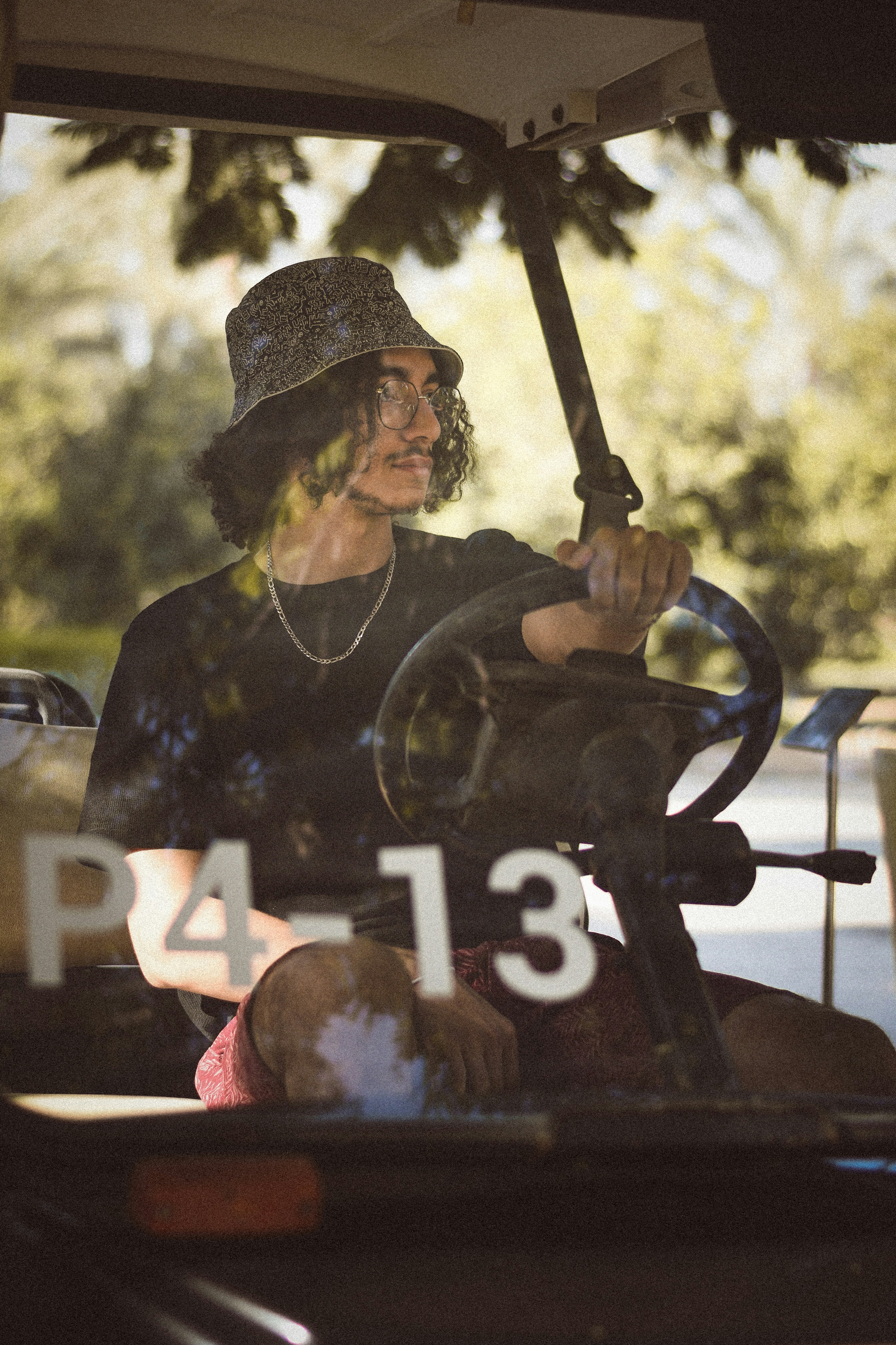 Coil of sunlight: a hat-wearing driver gazes off to the left from behind a steering wheel