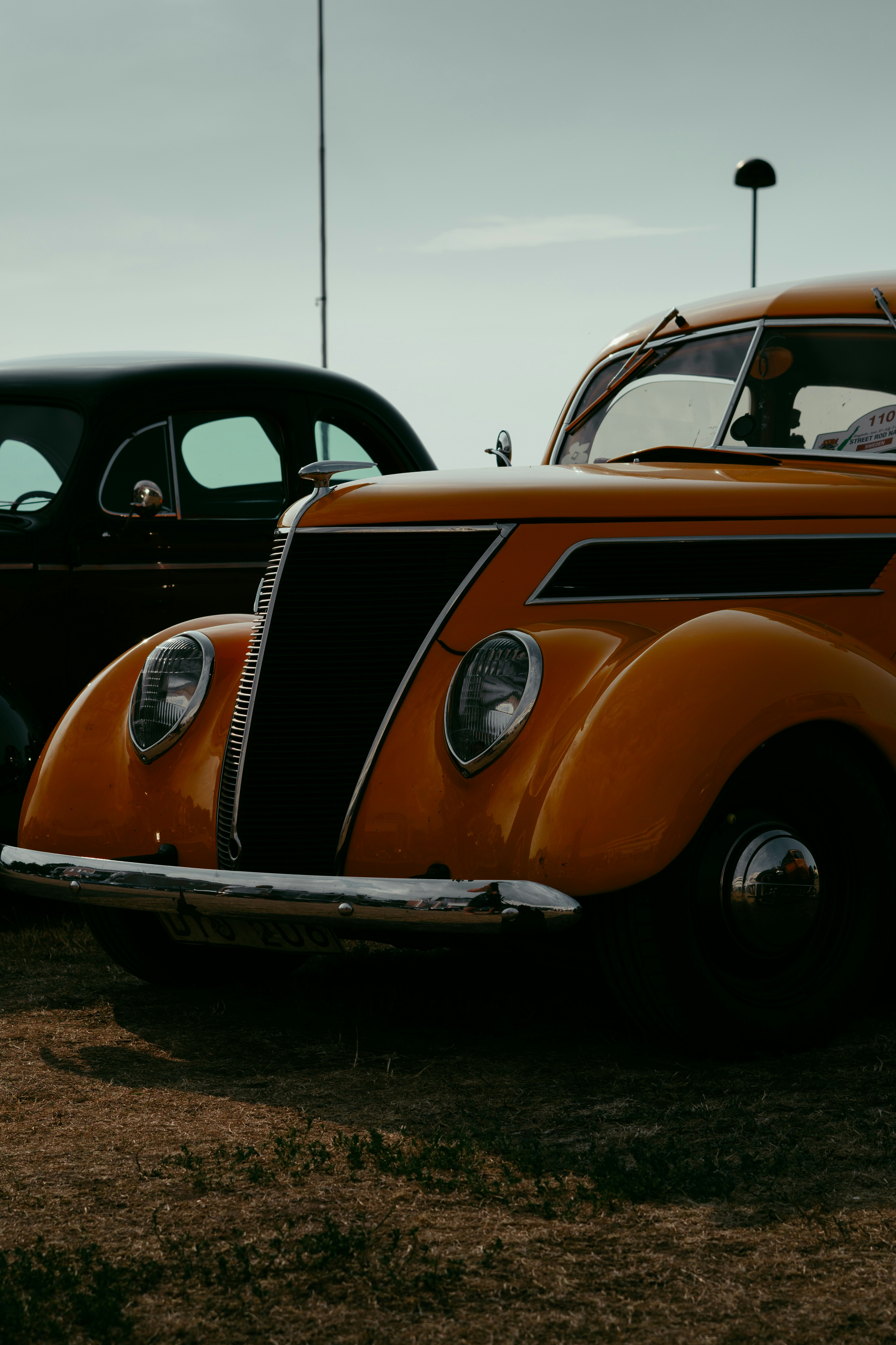 Sunlit Ember: Front-Grille Portrait of a Vintage Orange Car at a Car Show