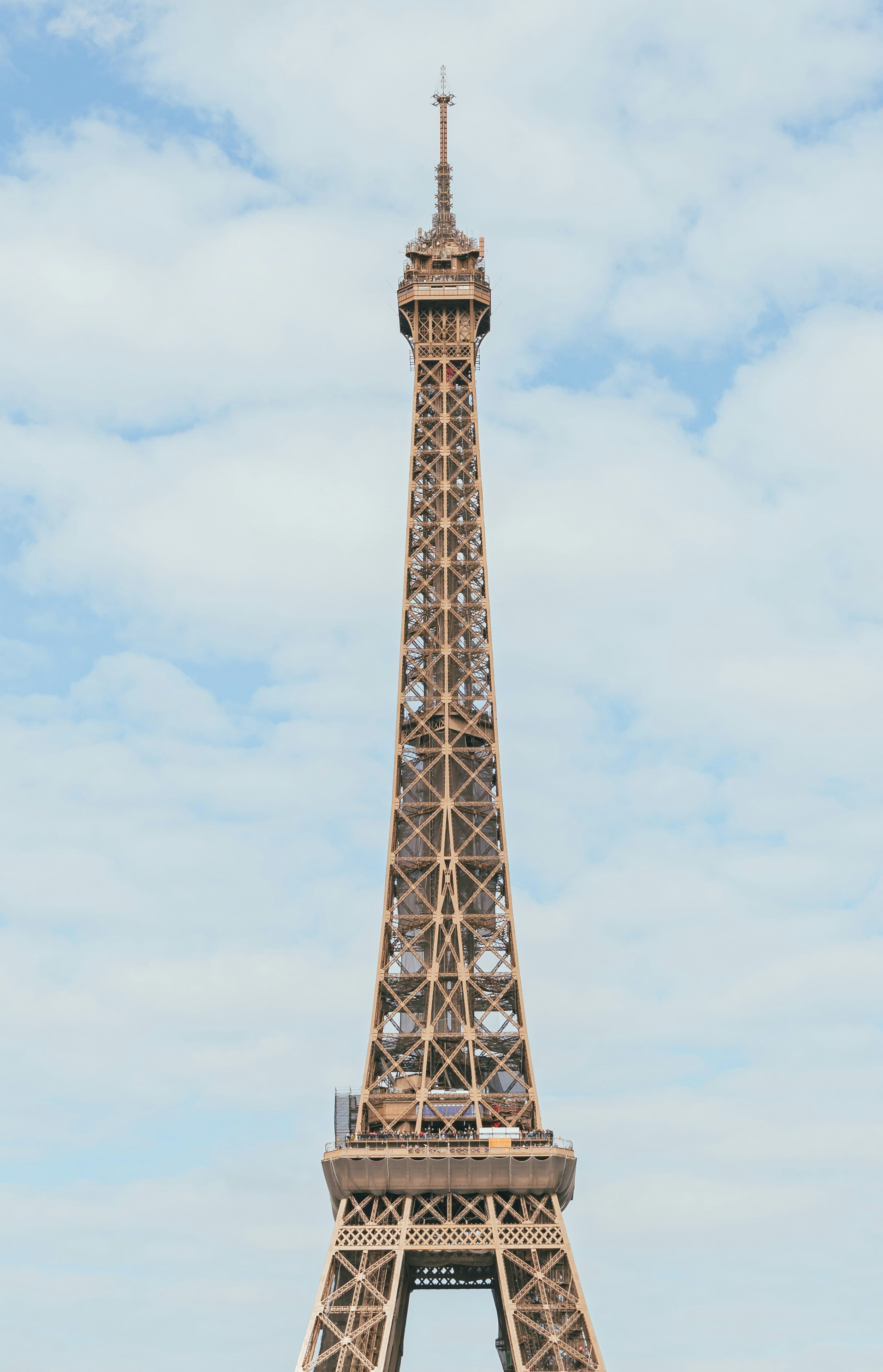 Eiffel Tower rising prominently against a backdrop of soft, scattered clouds, showcasing its intricate iron lattice design.
