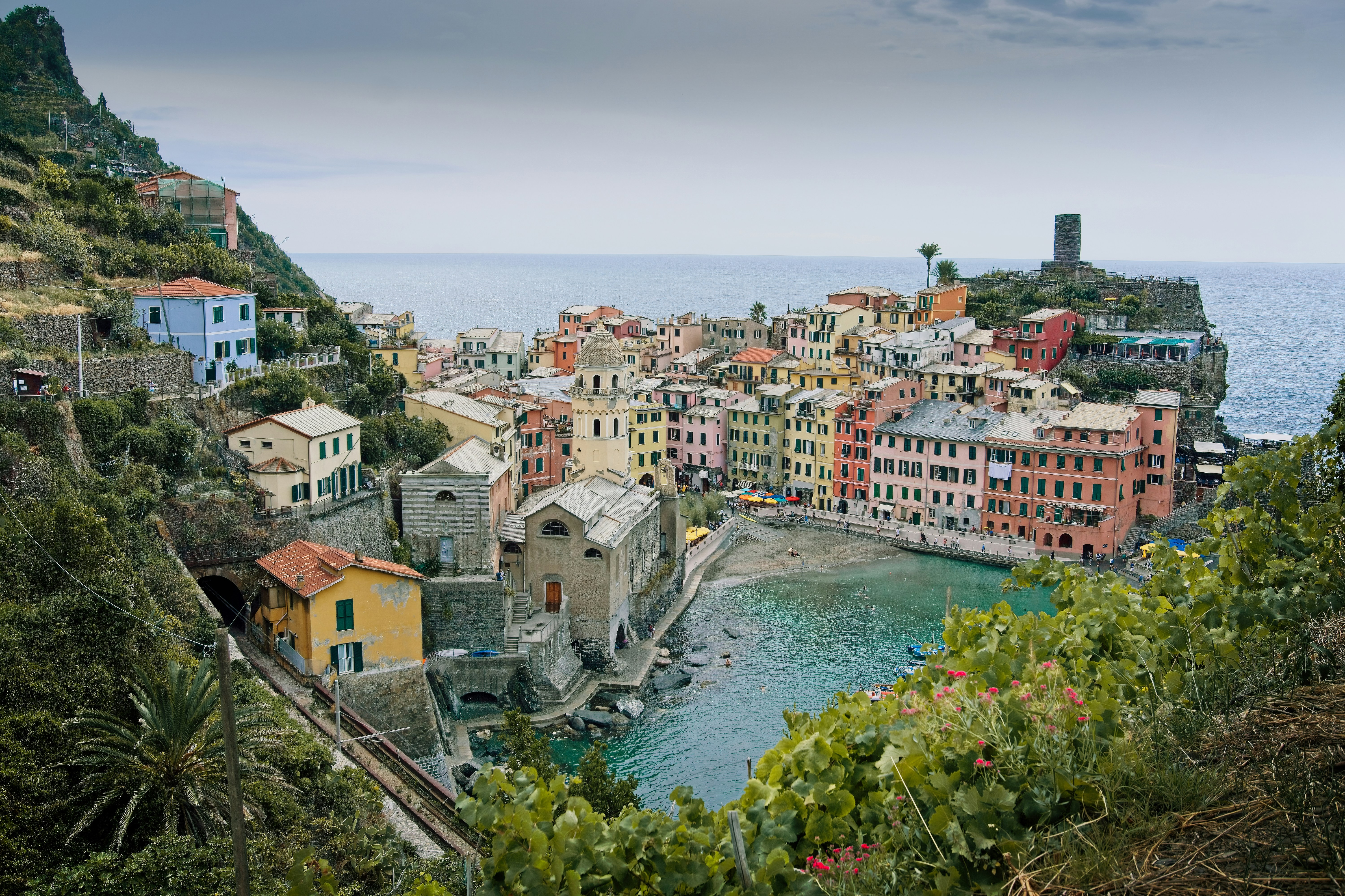Colorful coastal village of Vernazza nestled between lush hills and the sea under a cloudy sky.