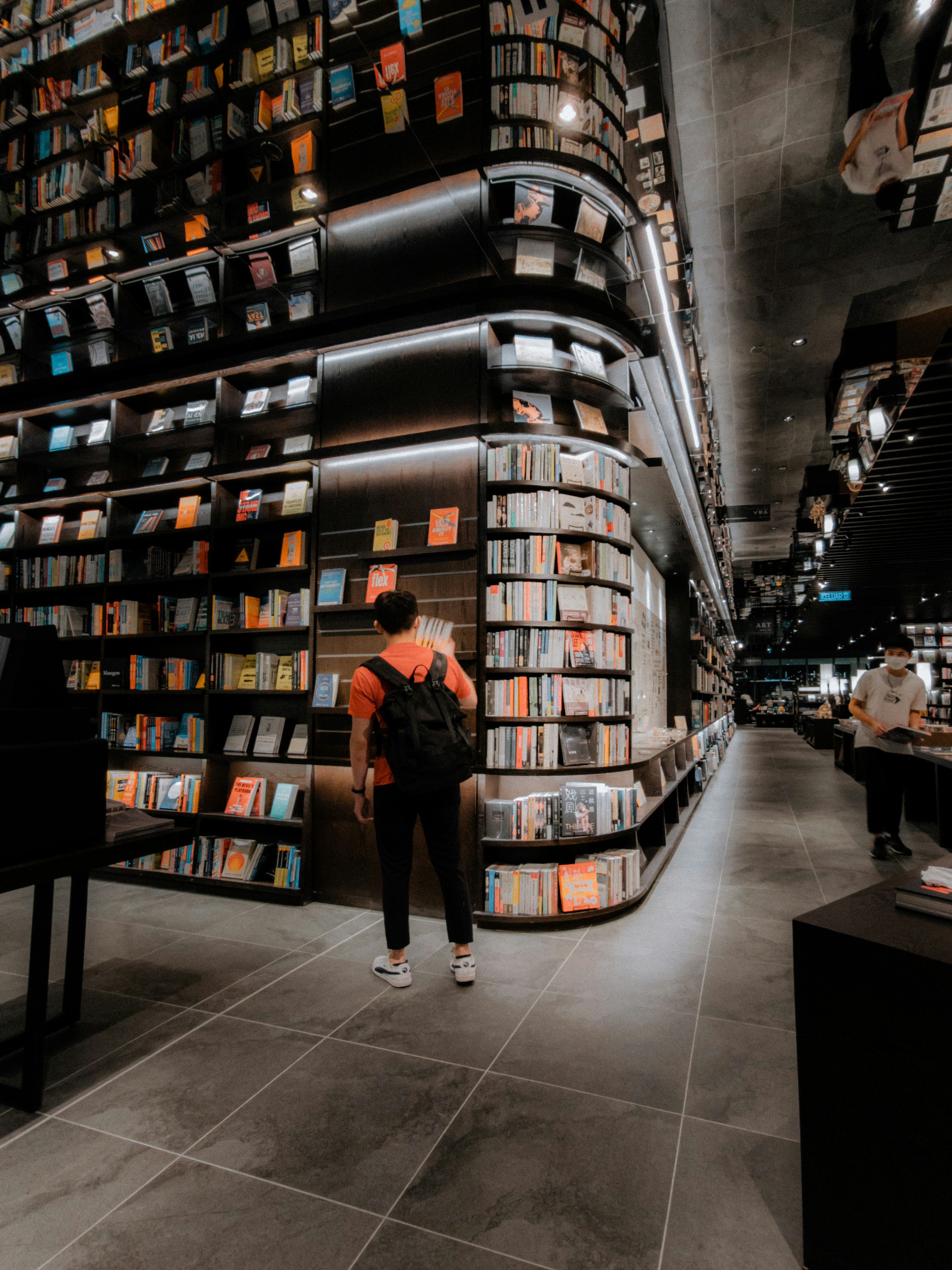 Person standing in a modern bookstore surrounded by towering shelves filled with colorful books.